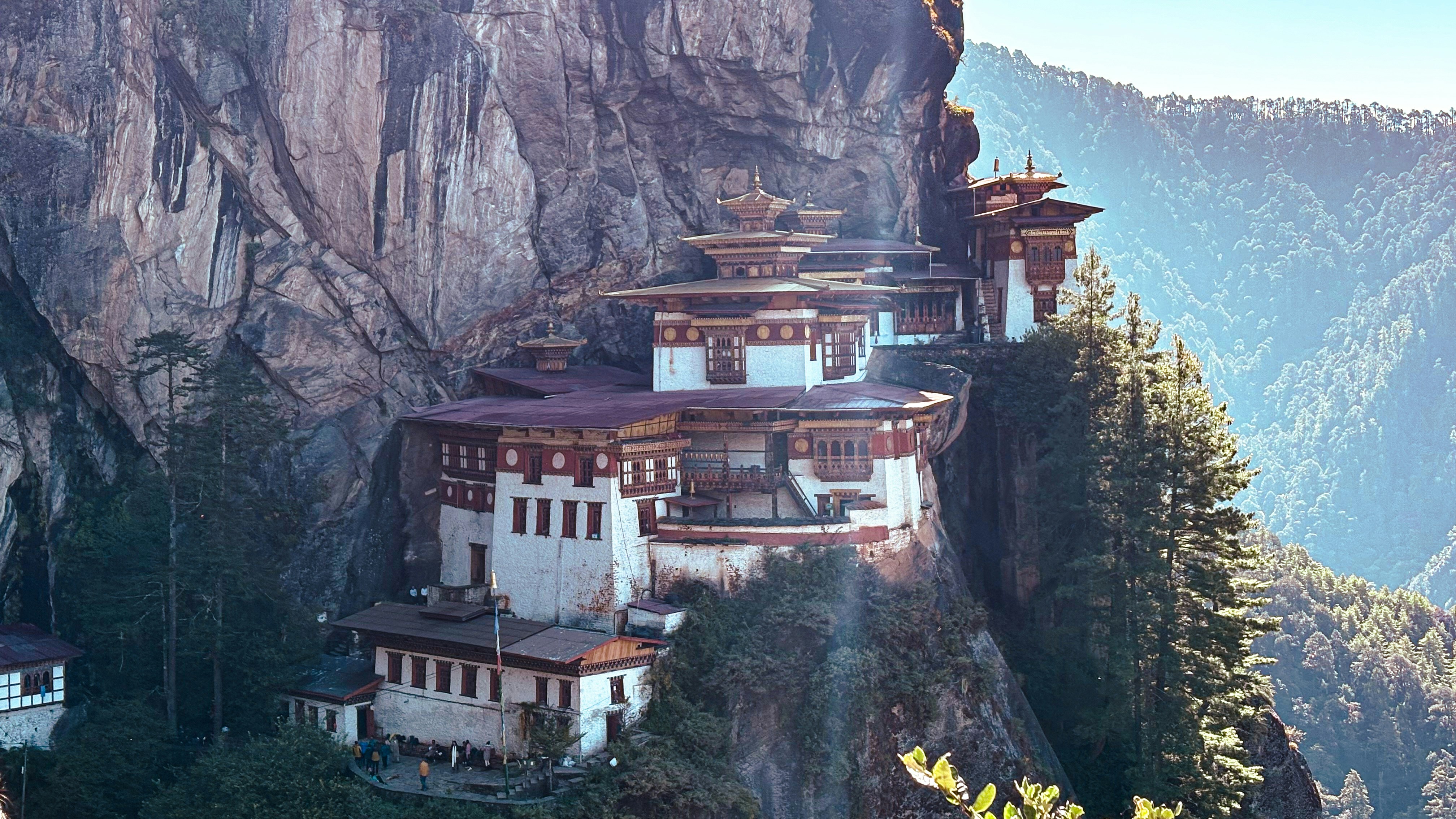 Tiger's Nest Monastery clings dramatically to a cliffside above a lush Himalayan forest, bathed in soft morning light that enhances its sacred and serene presence.