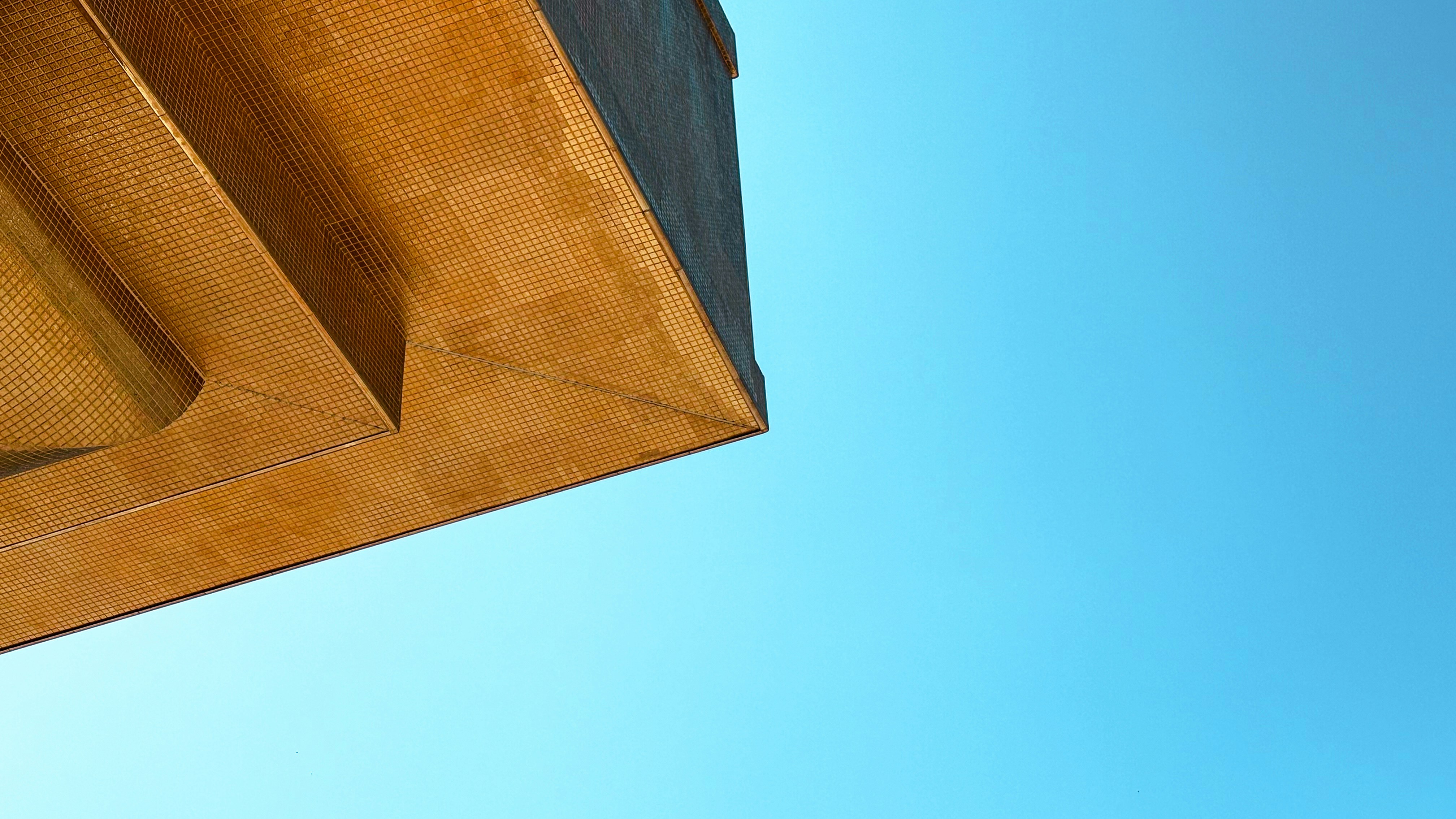 A striking golden building catches the sunlight in Thimphu, Bhutan, its clean geometric lines and textured surface standing out boldly against a clear blue sky. | Brown paper bag against a clear blue sky