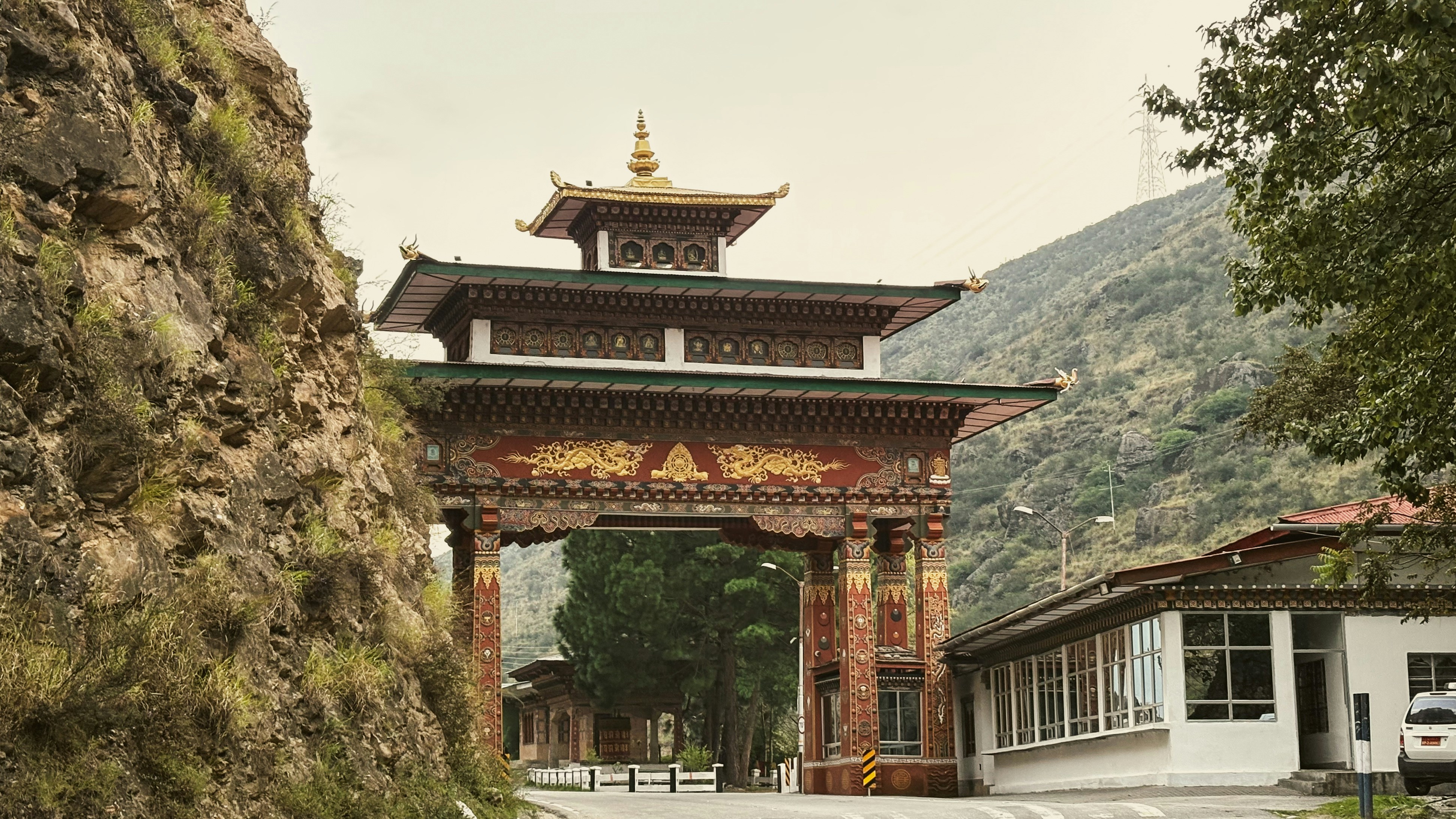 Traditional Bhutanese archway adorned with intricate carvings, nestled among lush greenery and rocky terrain.