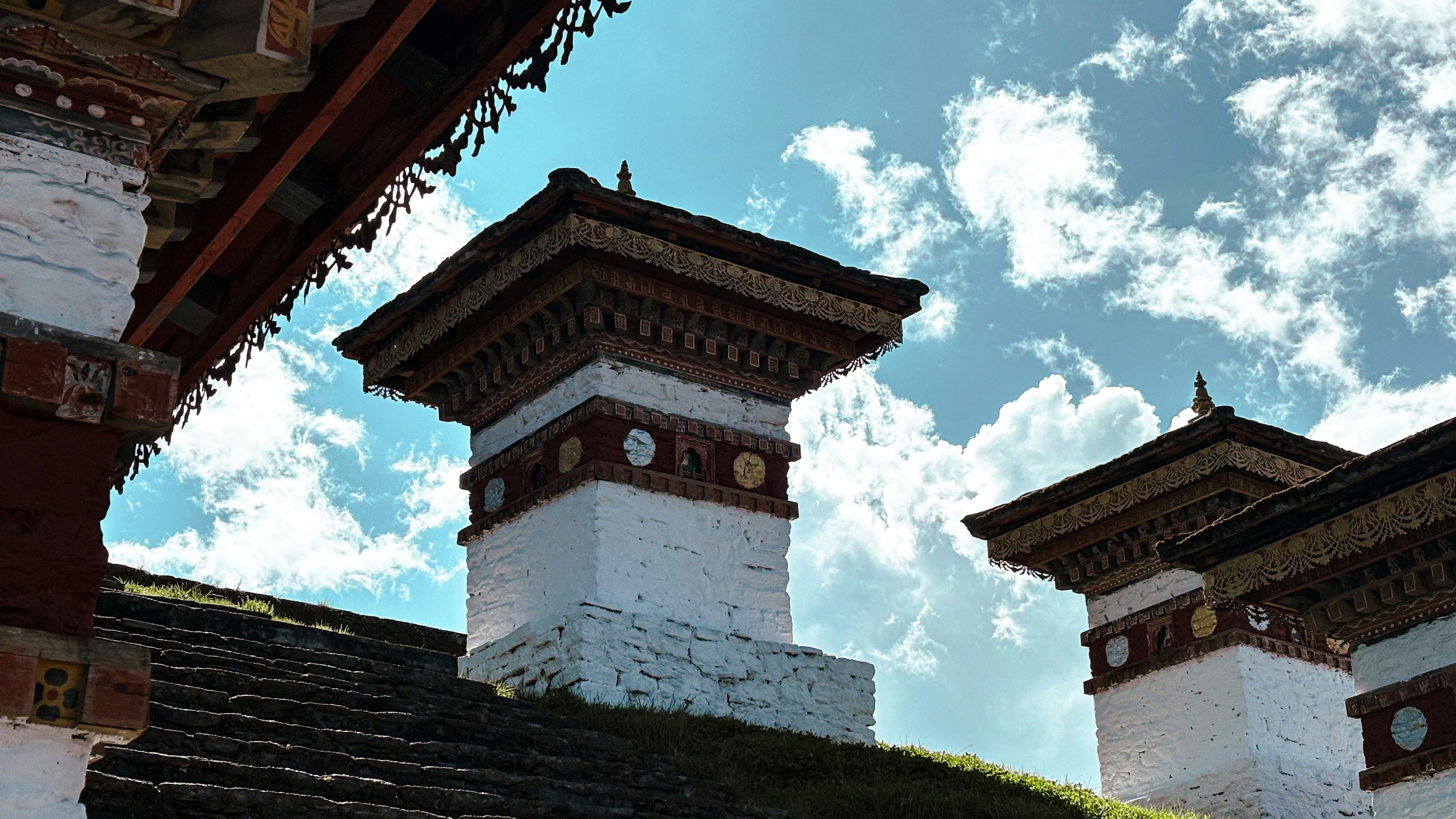 Sunlight illuminates the white stupas of Dochula Pass against a bright blue sky, highlighting their intricate details and serene Himalayan setting. | Traditional bhutanese stupas against a blue sky.