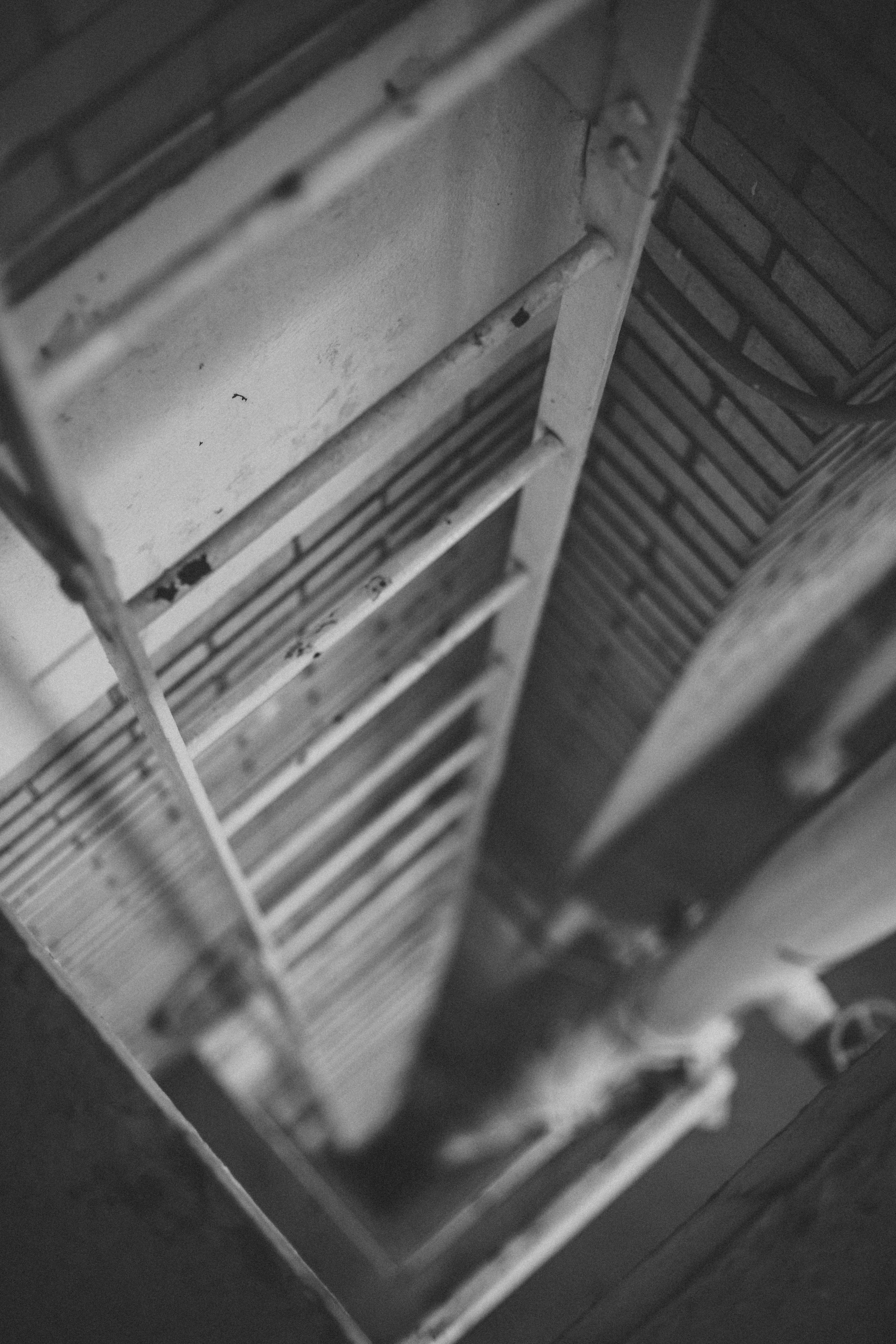 A monochrome view looking down a metal ladder in an industrial setting, emphasizing the depth and structure of the space.