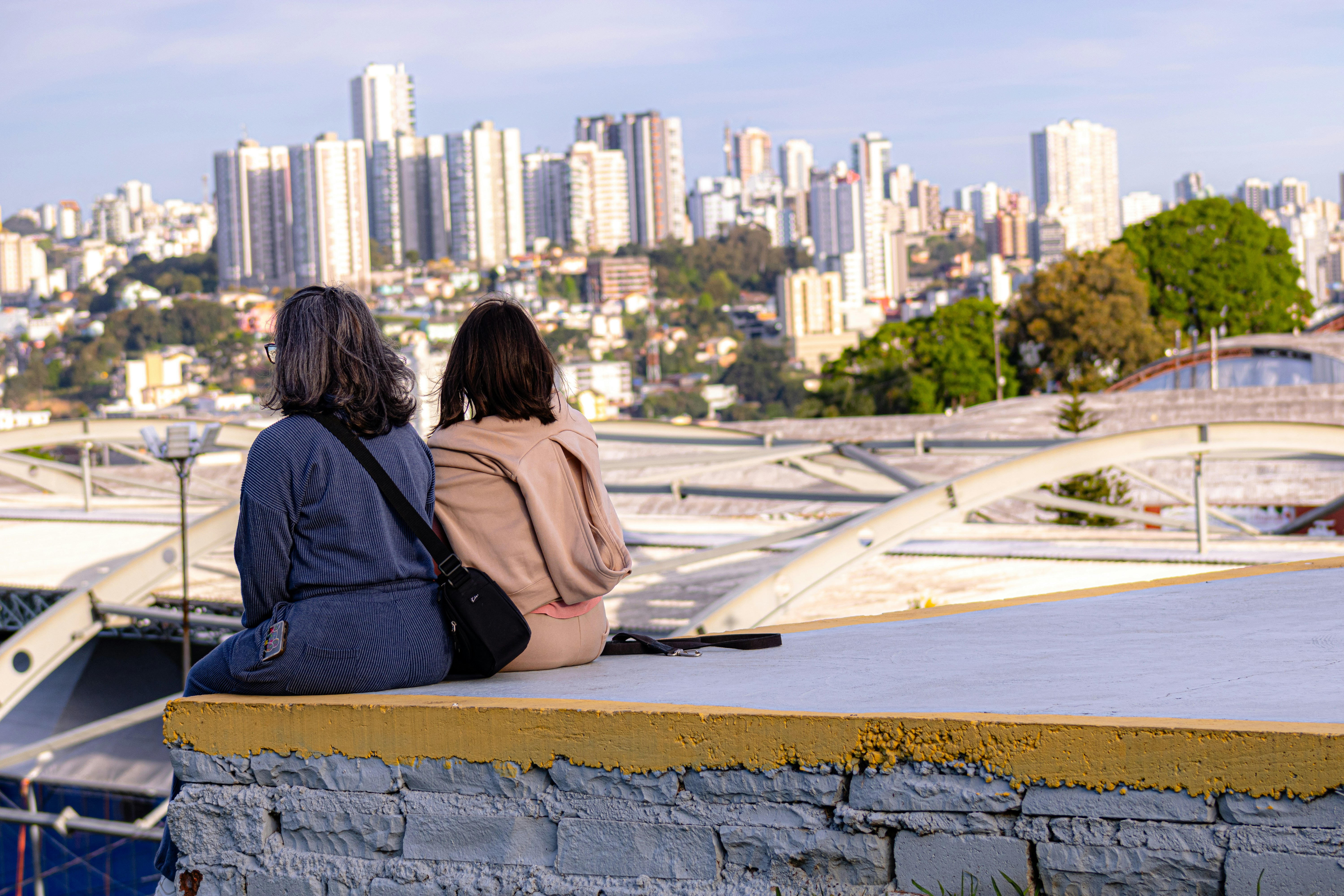 Two people sit on a ledge overlooking a city.