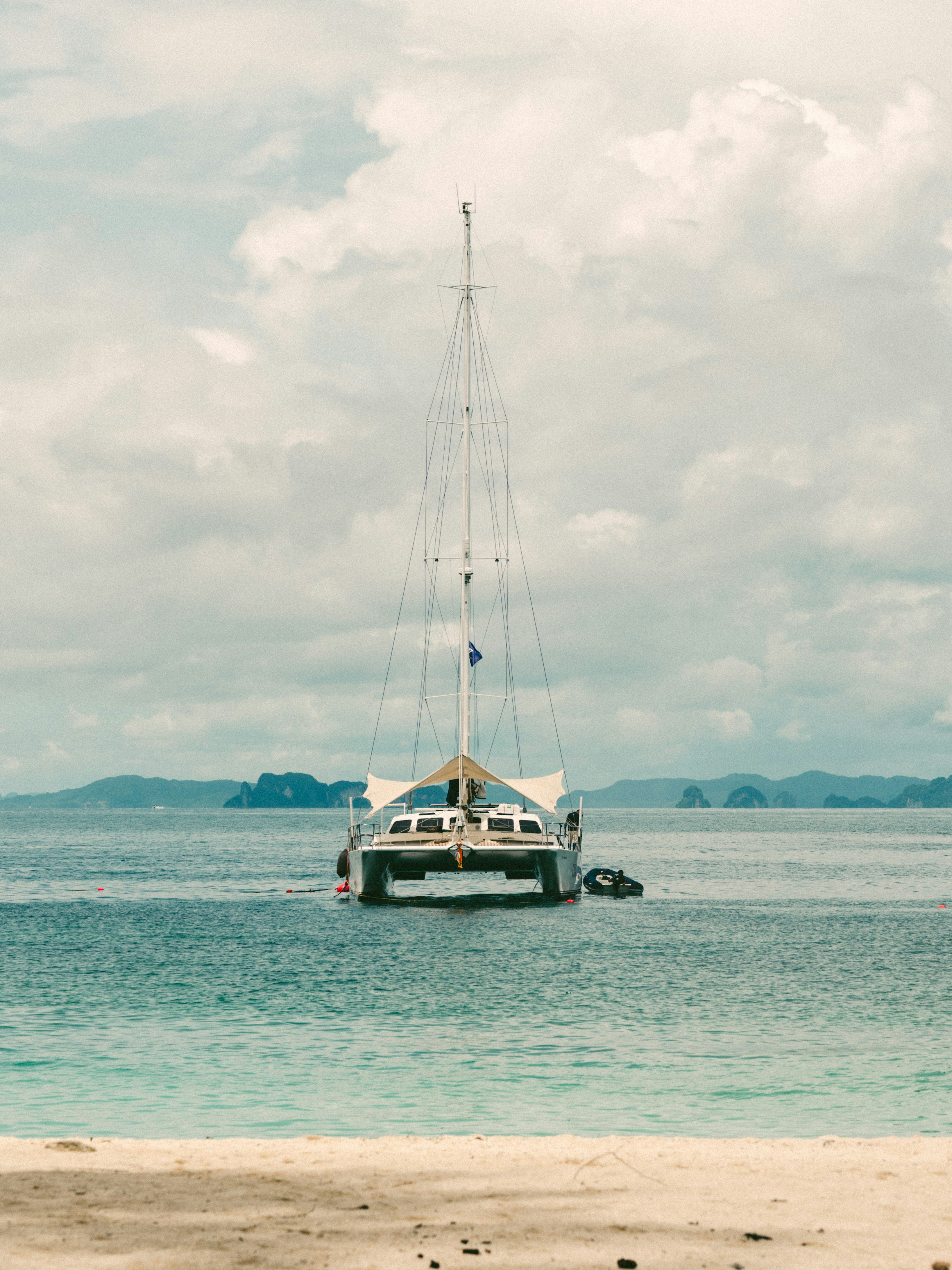 A catamaran anchored in tranquil waters, framed by distant islands and a cloudy sky. The scene evokes a sense of calm and adventure.