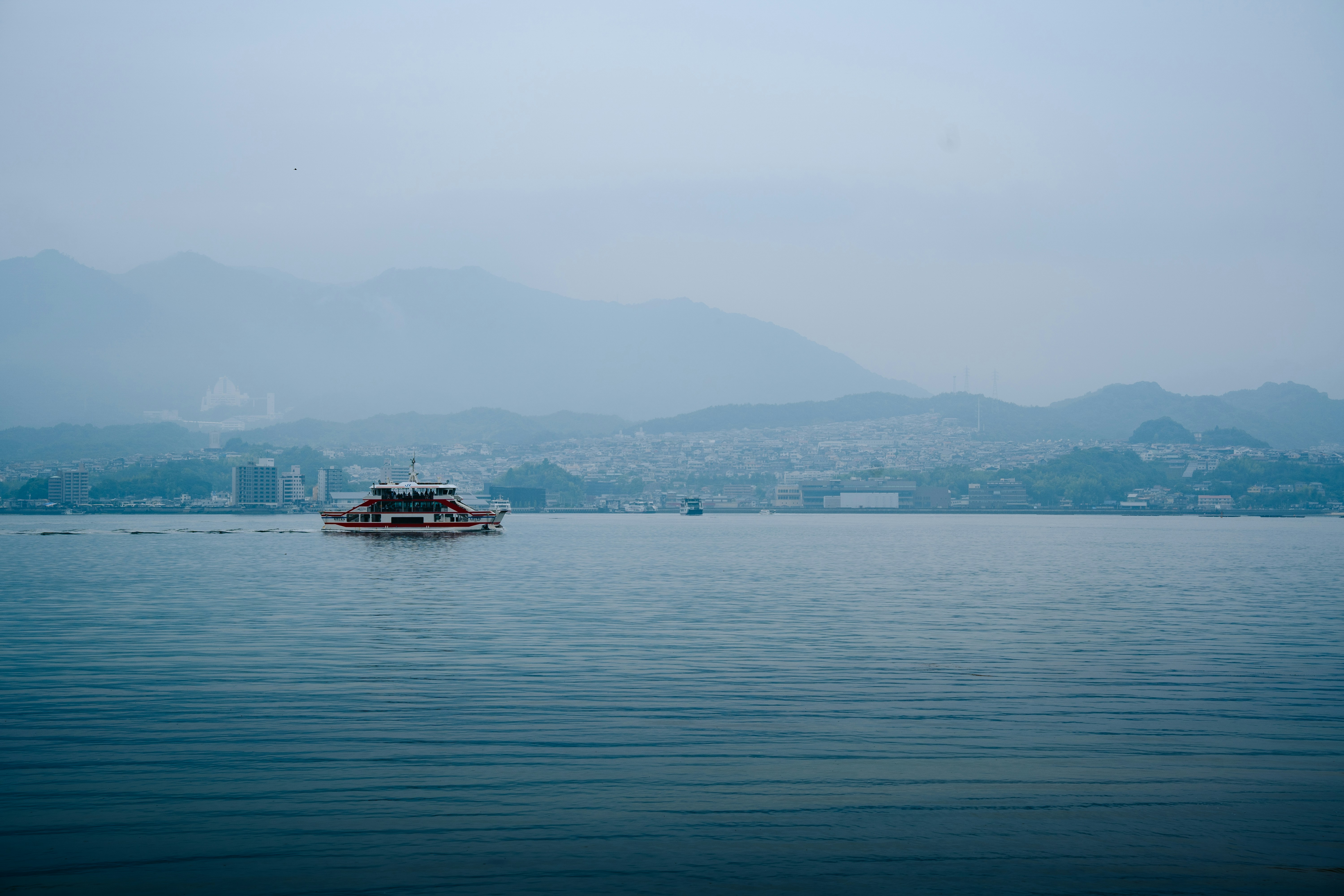 A boat glides across a tranquil body of water, framed by distant mountains and a hazy skyline. The scene captures a moment of calm amidst nature's embrace.