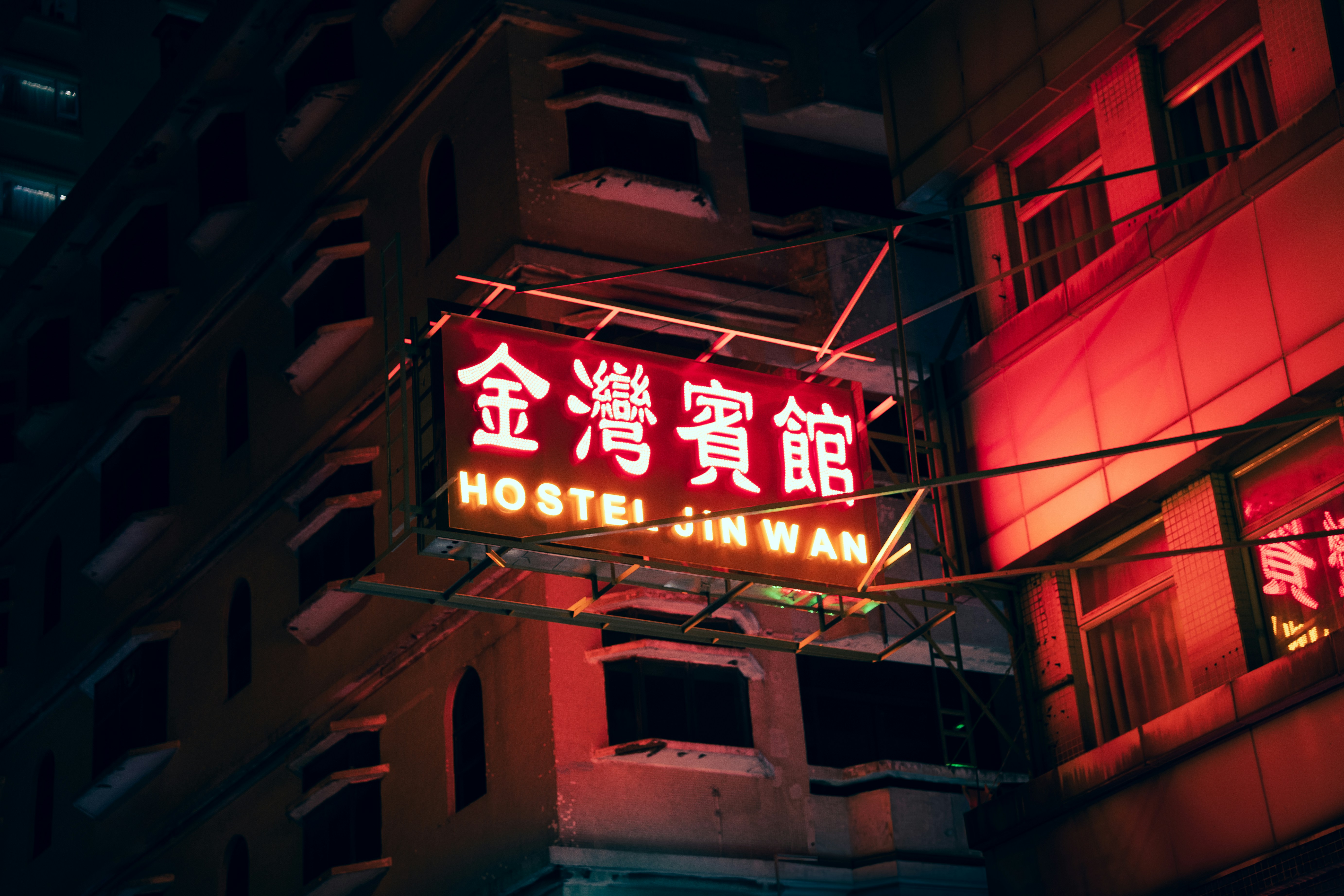 Vibrant neon sign for Jin Wan Hostel illuminated against a dark building backdrop at night.