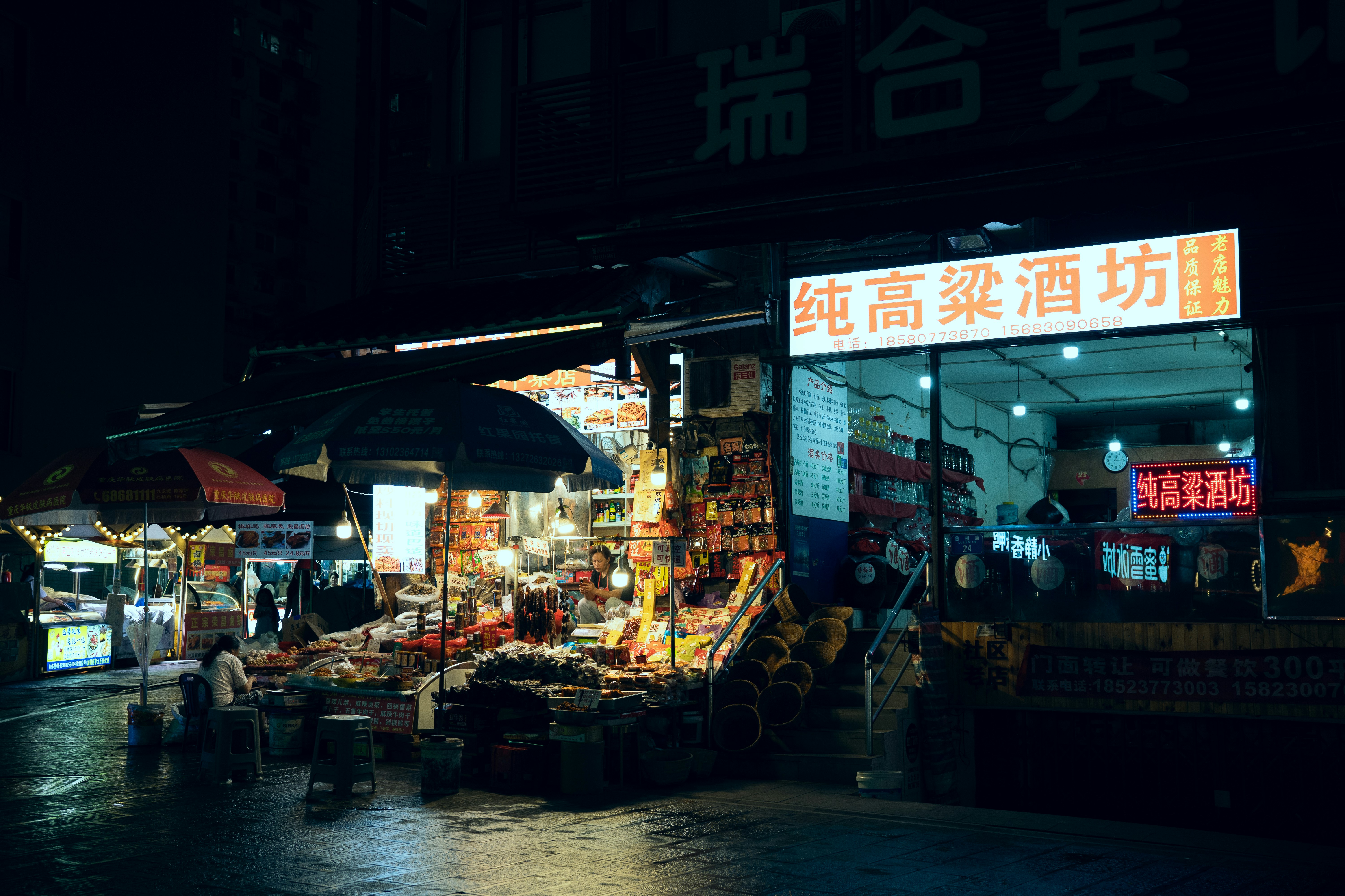 Vibrant street market illuminated at night, showcasing a variety of goods and colorful signage. The scene captures the bustling atmosphere of urban commerce.