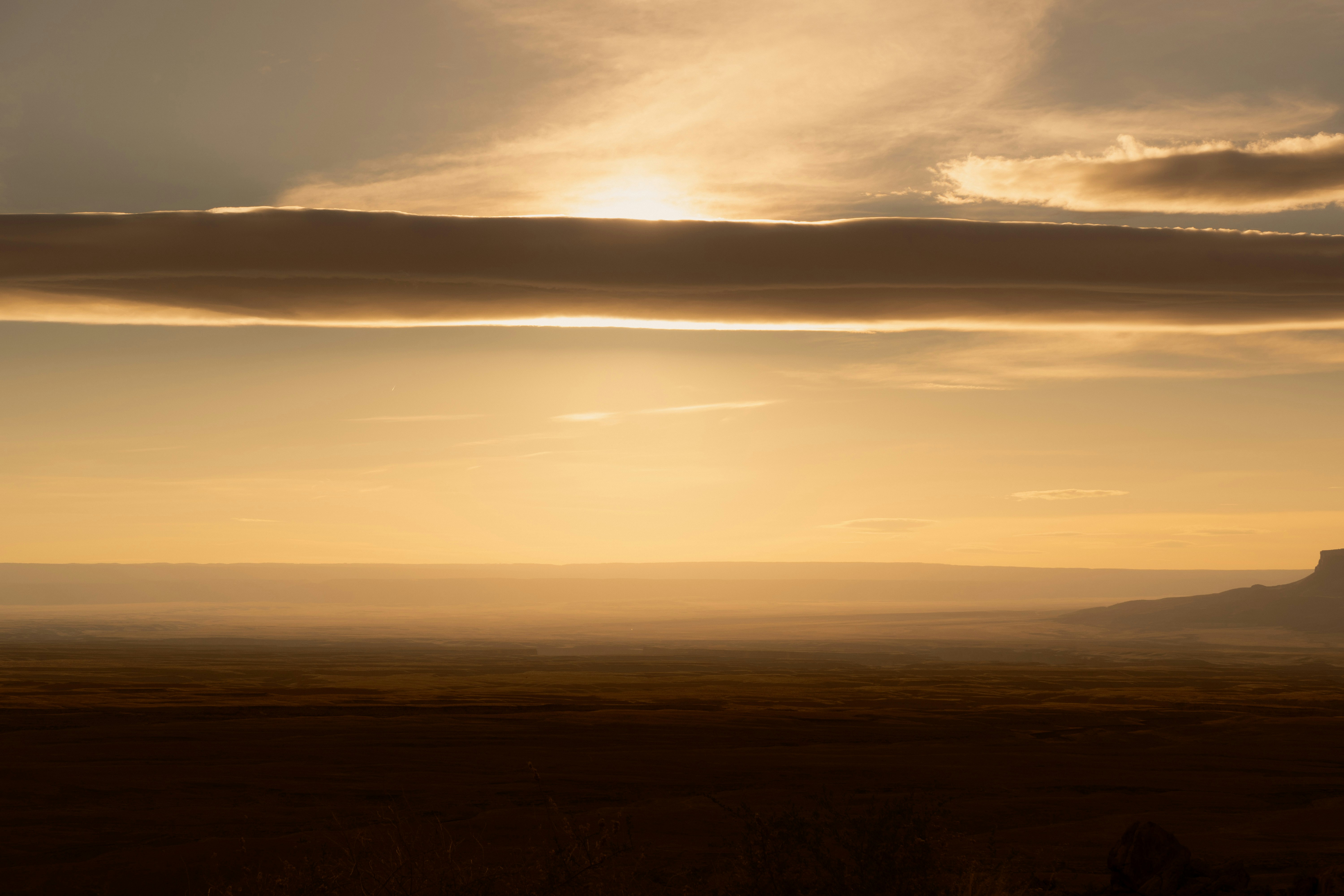 Golden hues of sunset stretch across a vast landscape, with a prominent cloud formation enhancing the serene atmosphere.