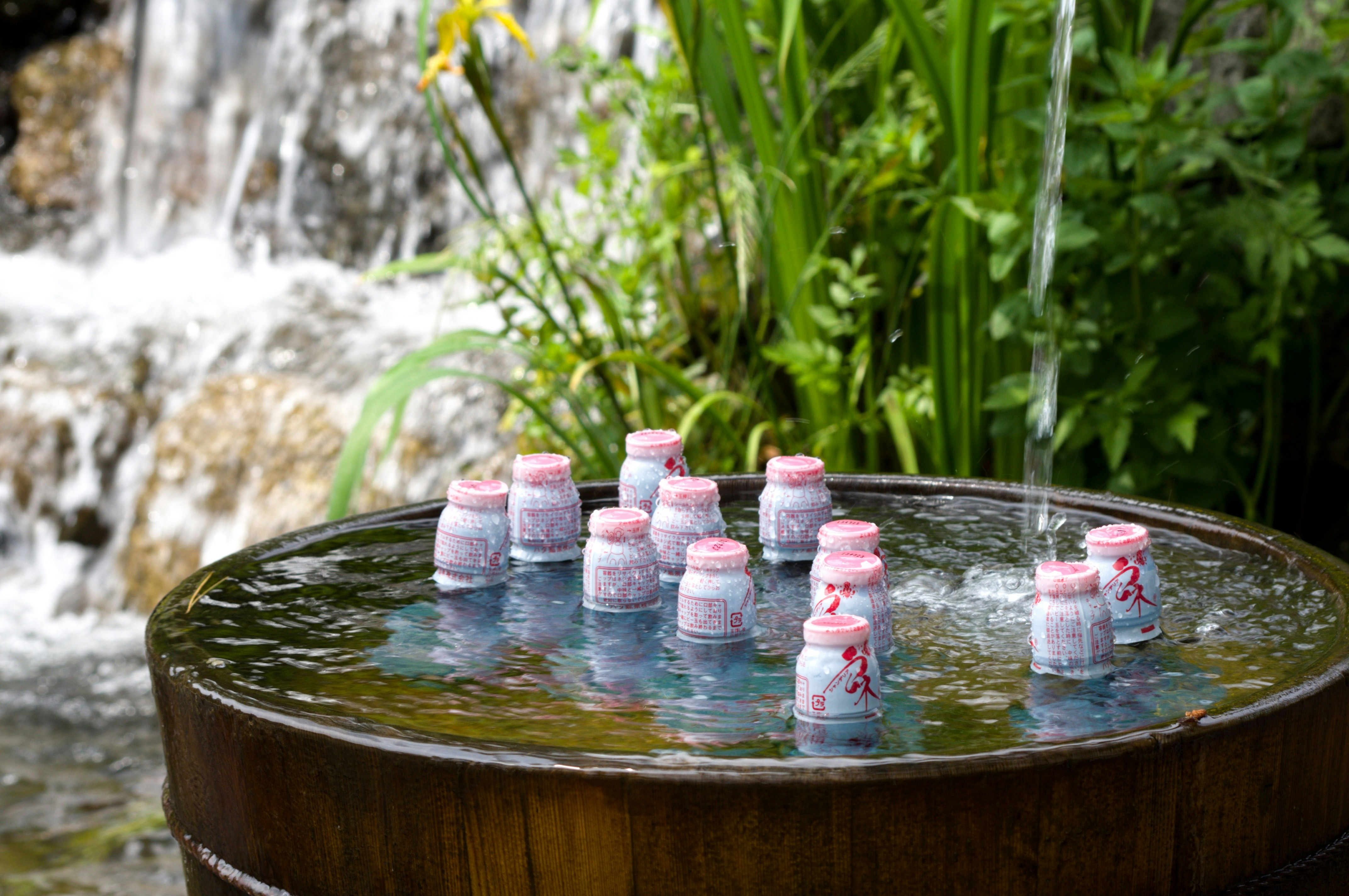 Small bottles floating in a wooden basin near waterfall