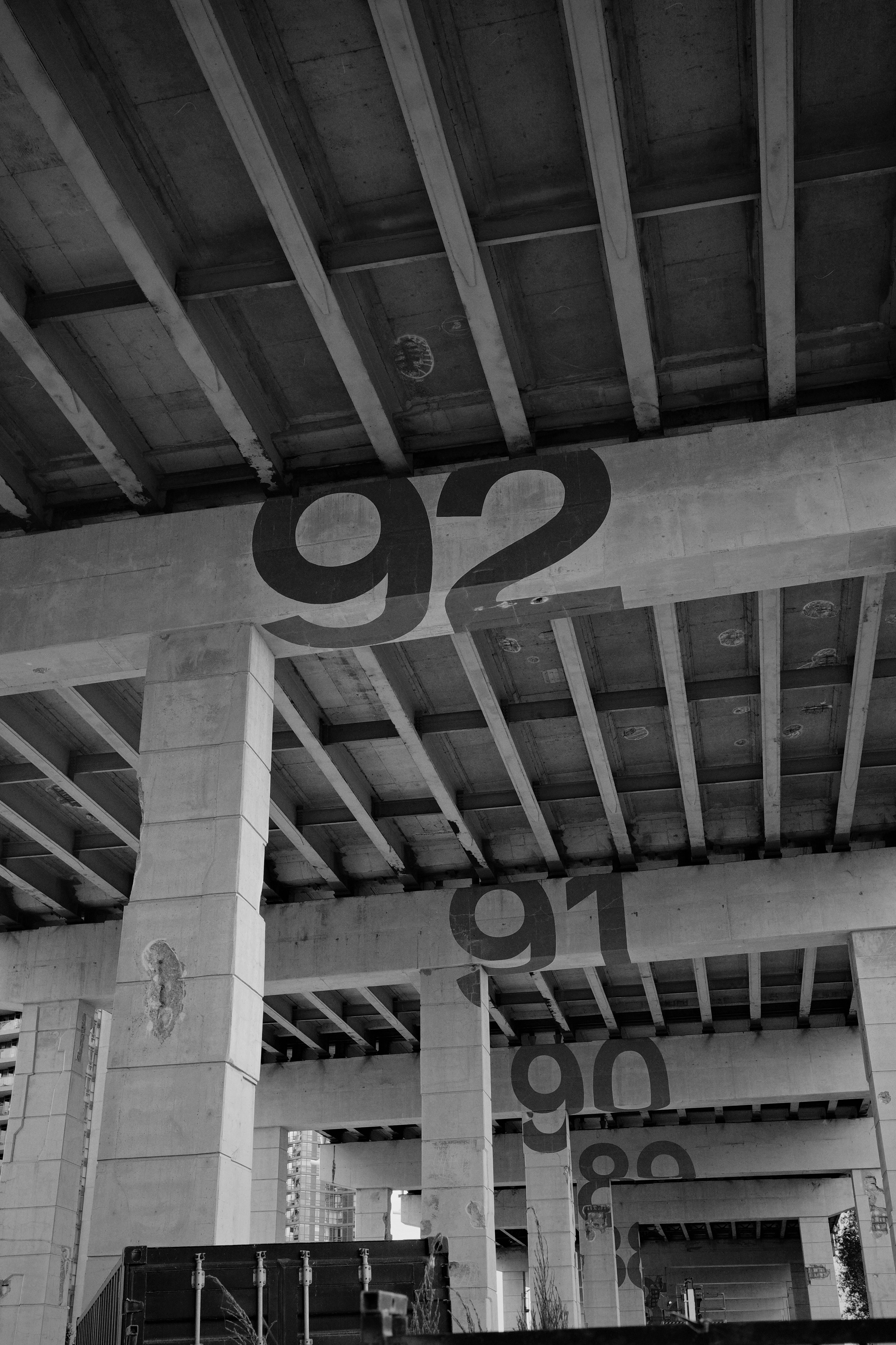 Large, bold numbers painted on concrete pillars beneath an overpass, creating a striking urban scene in monochrome.