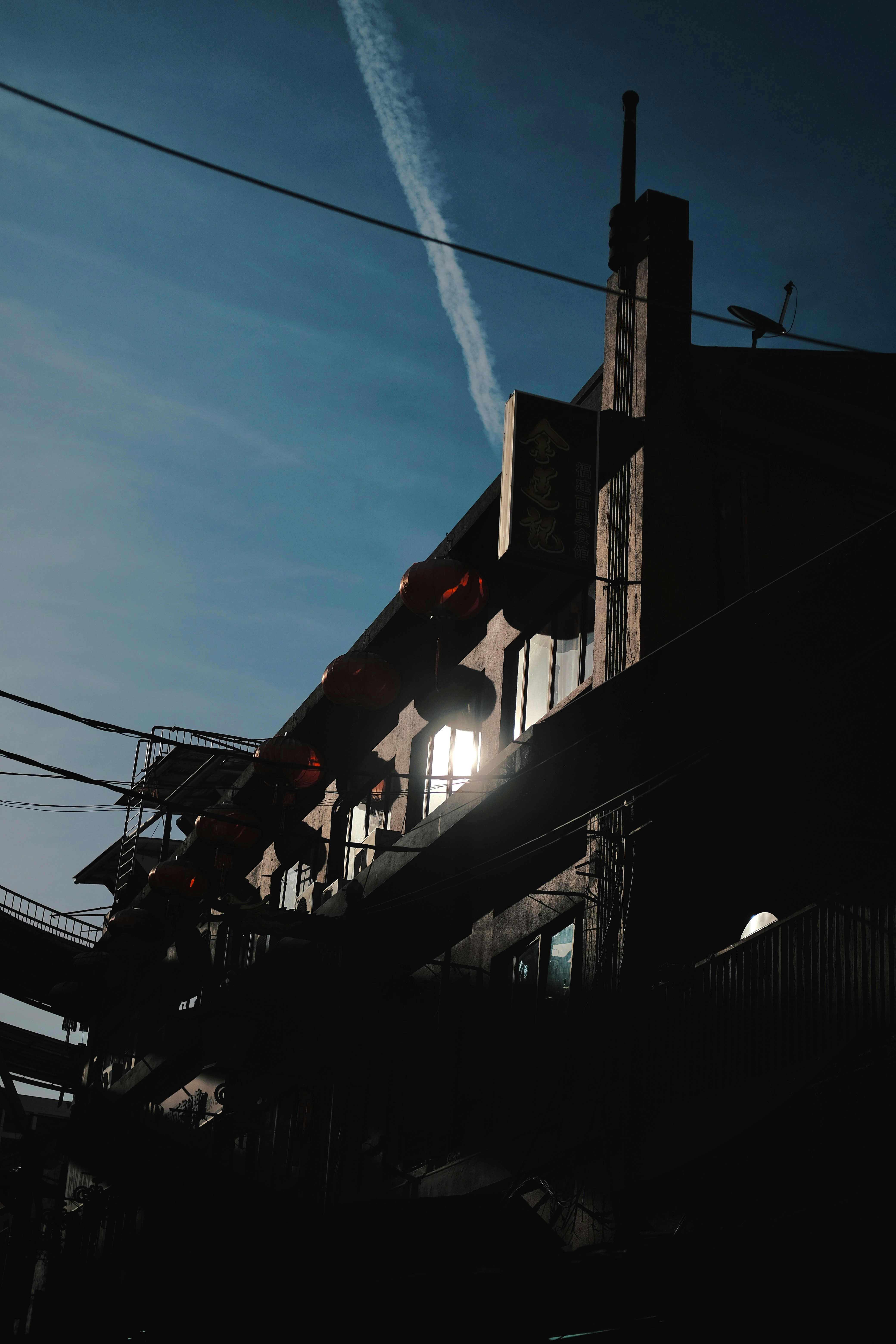 Silhouette of a building adorned with lanterns against a bright sky, capturing the interplay of light and architecture. The scene evokes a sense of urban tranquility.