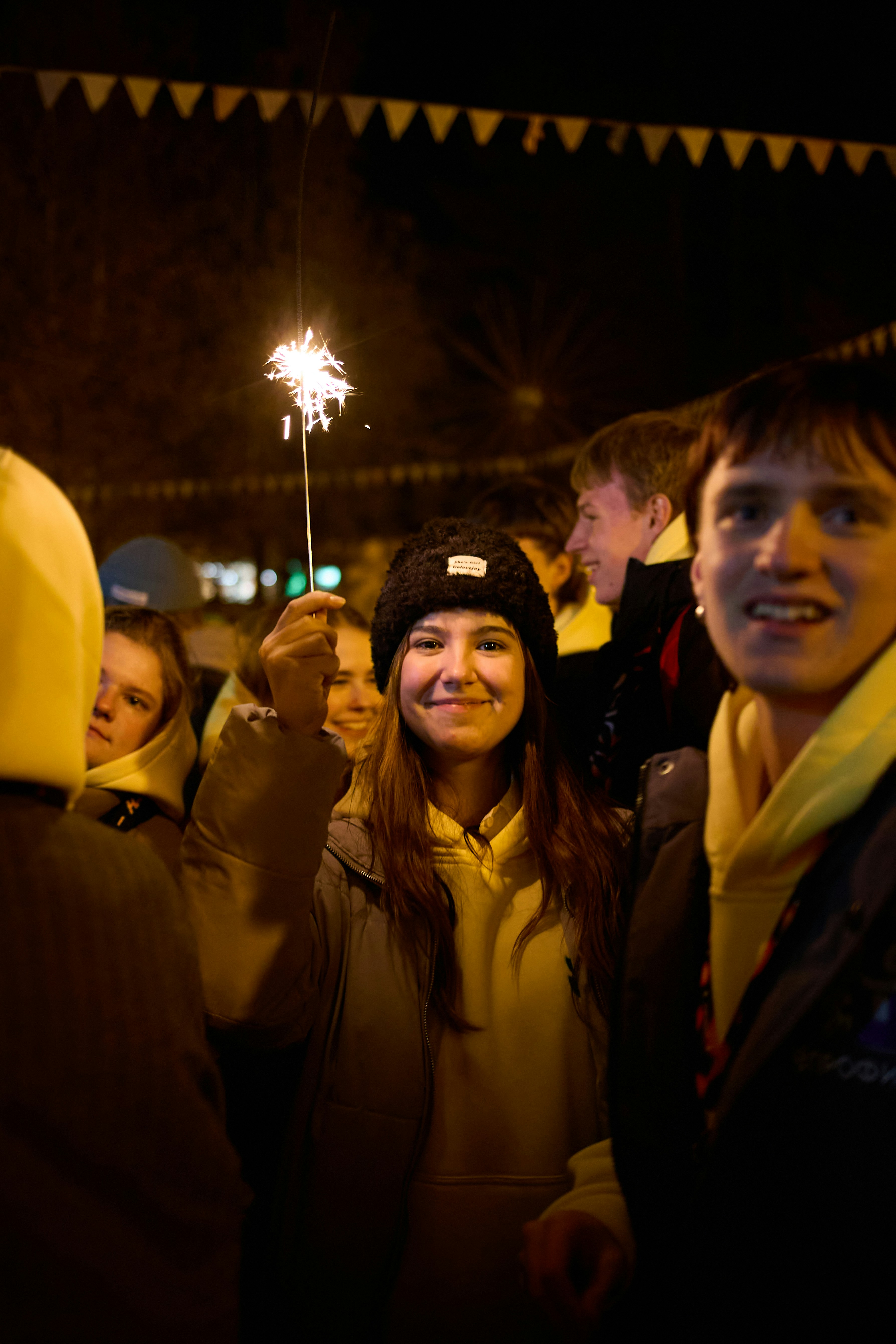 Young woman holding a sparkler with friends at night