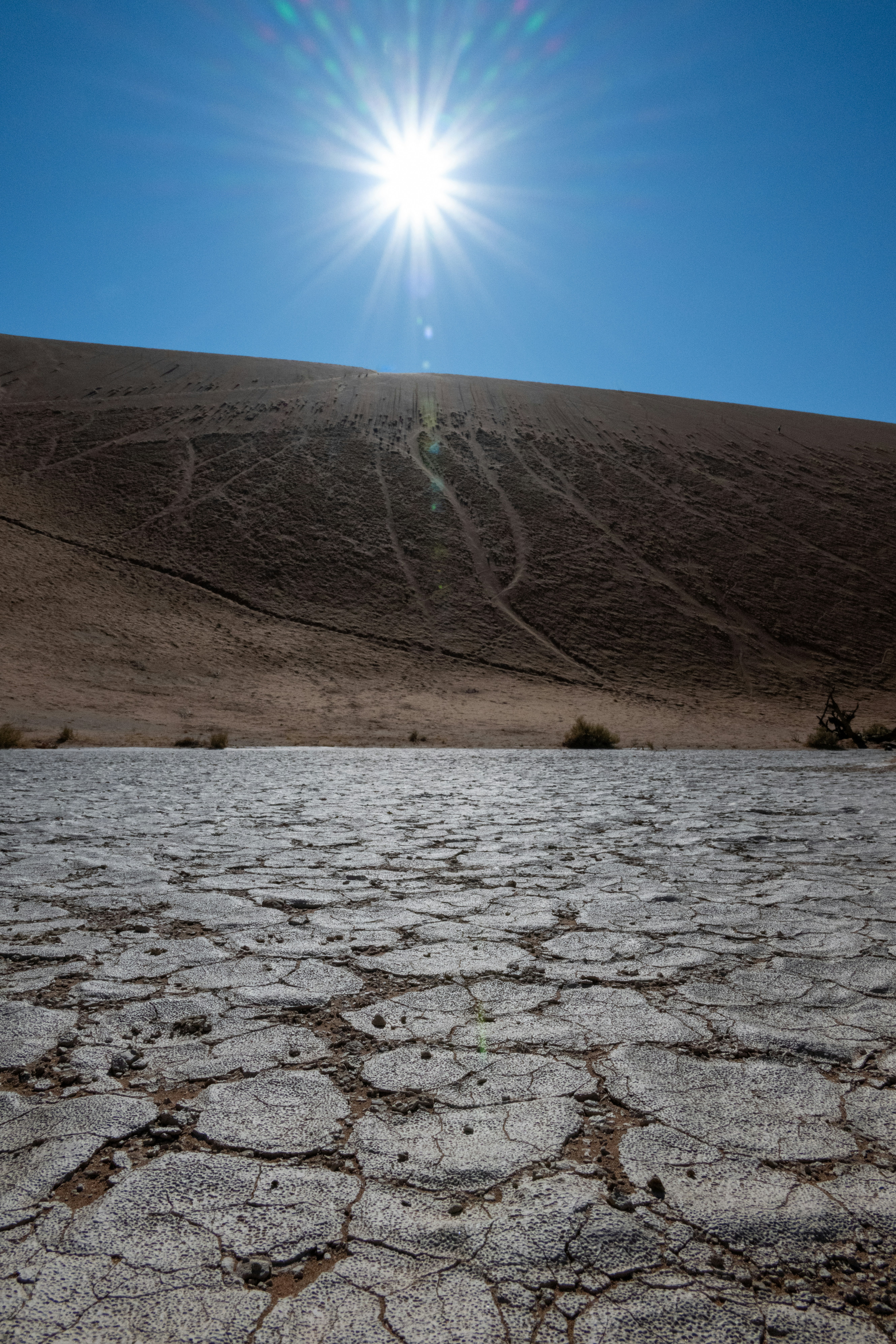 Bright sun shines over cracked earth and barren hill.