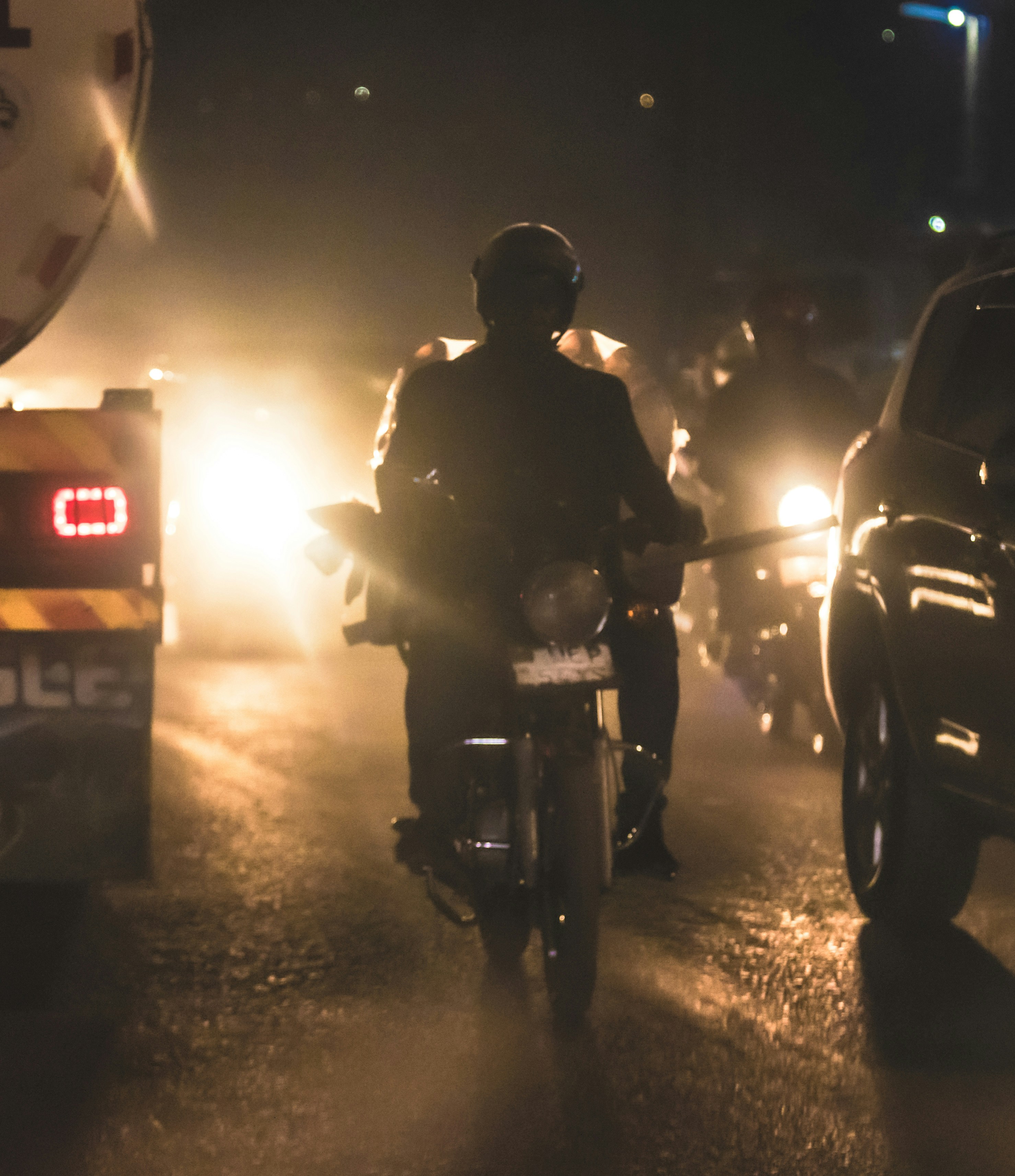Motorbike in heavy traffic at night | Motorcyclists ride through foggy, illuminated city streets at night.