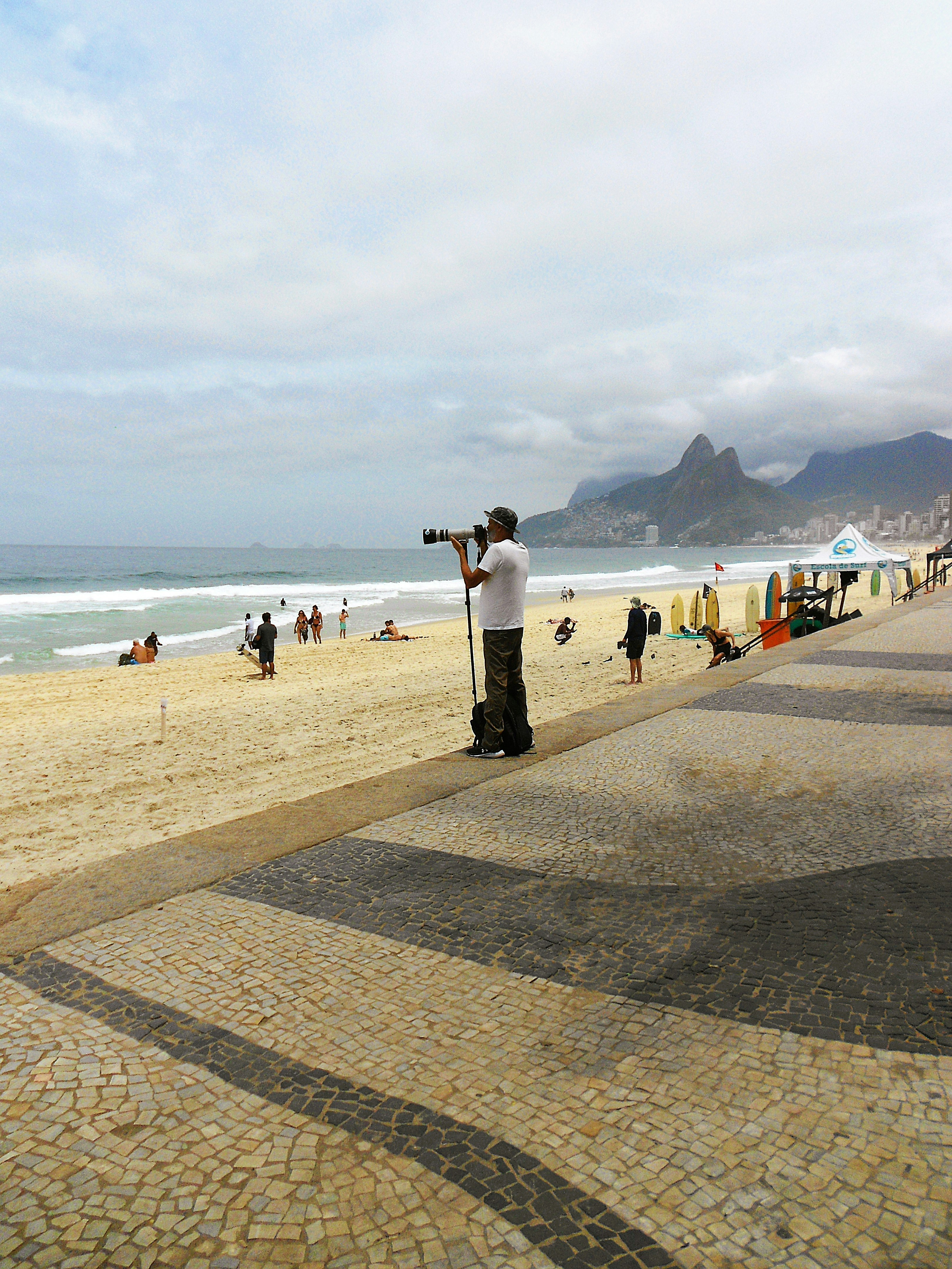 fotografo di surf | Man filming with camera on beach promenade.