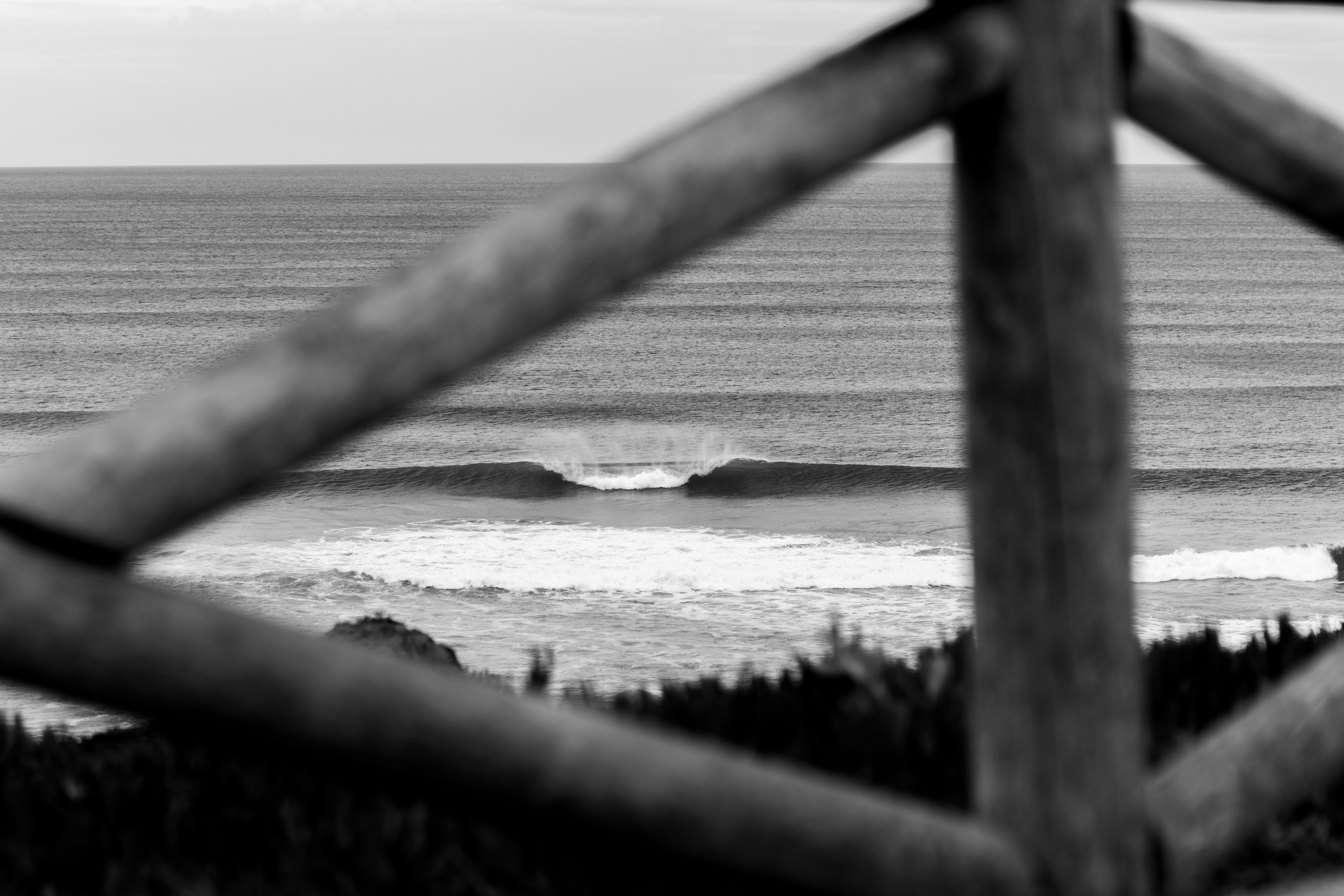 Wooden fence frames ocean waves breaking on shore