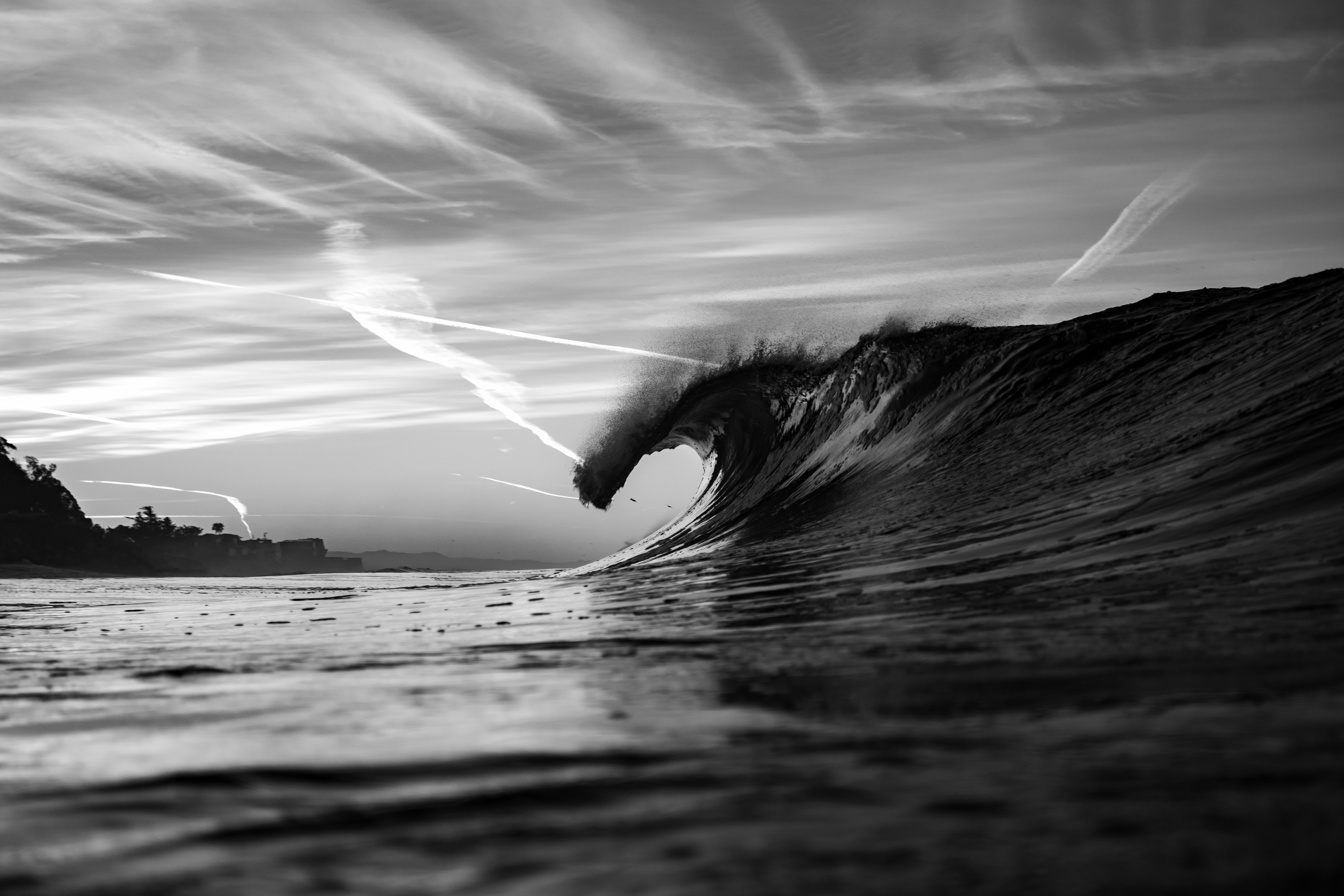 Dynamic ocean wave curling under a dramatic sky, captured in monochrome. The scene evokes the raw power and beauty of nature.