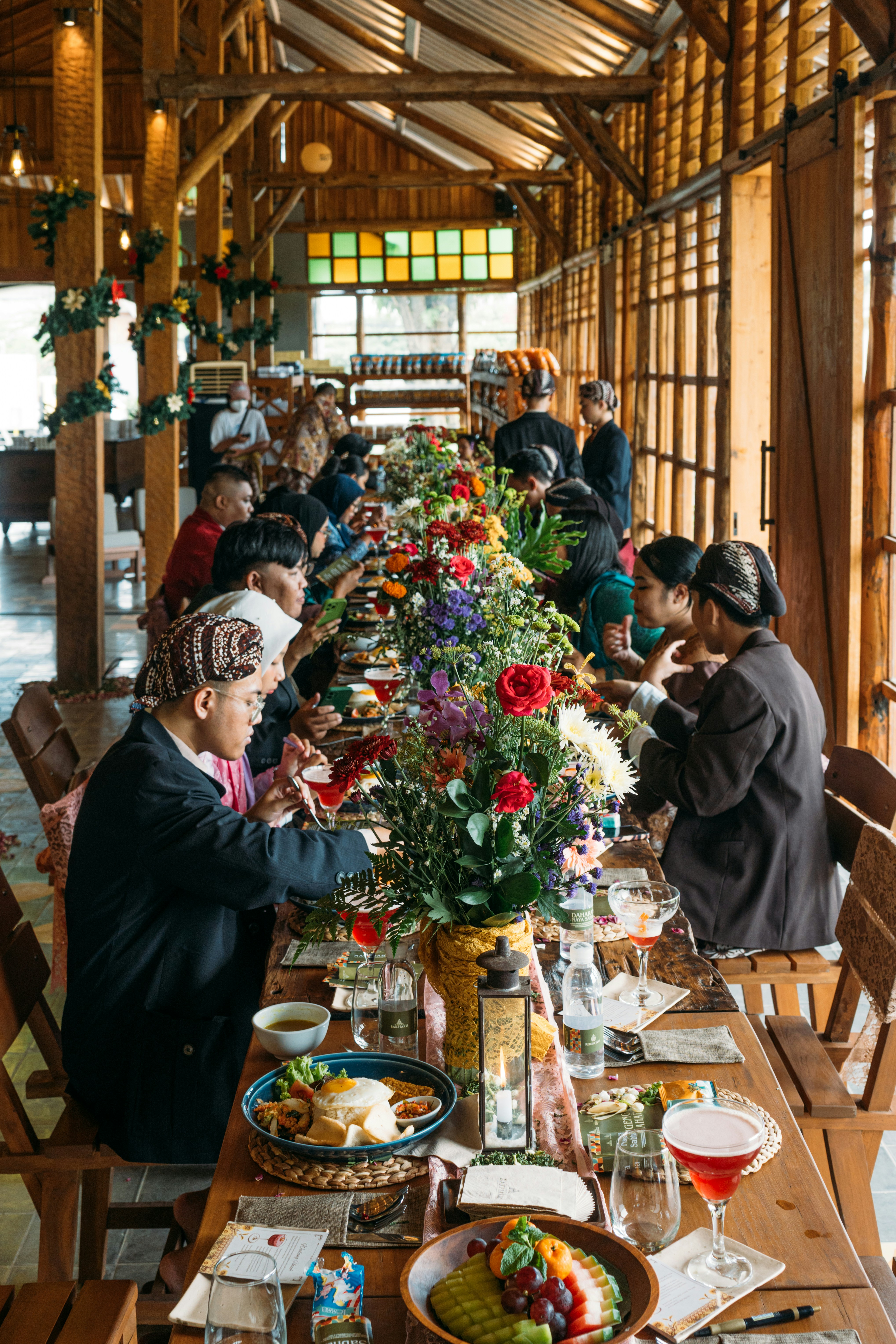 People gathered around a long table with food and flowers.