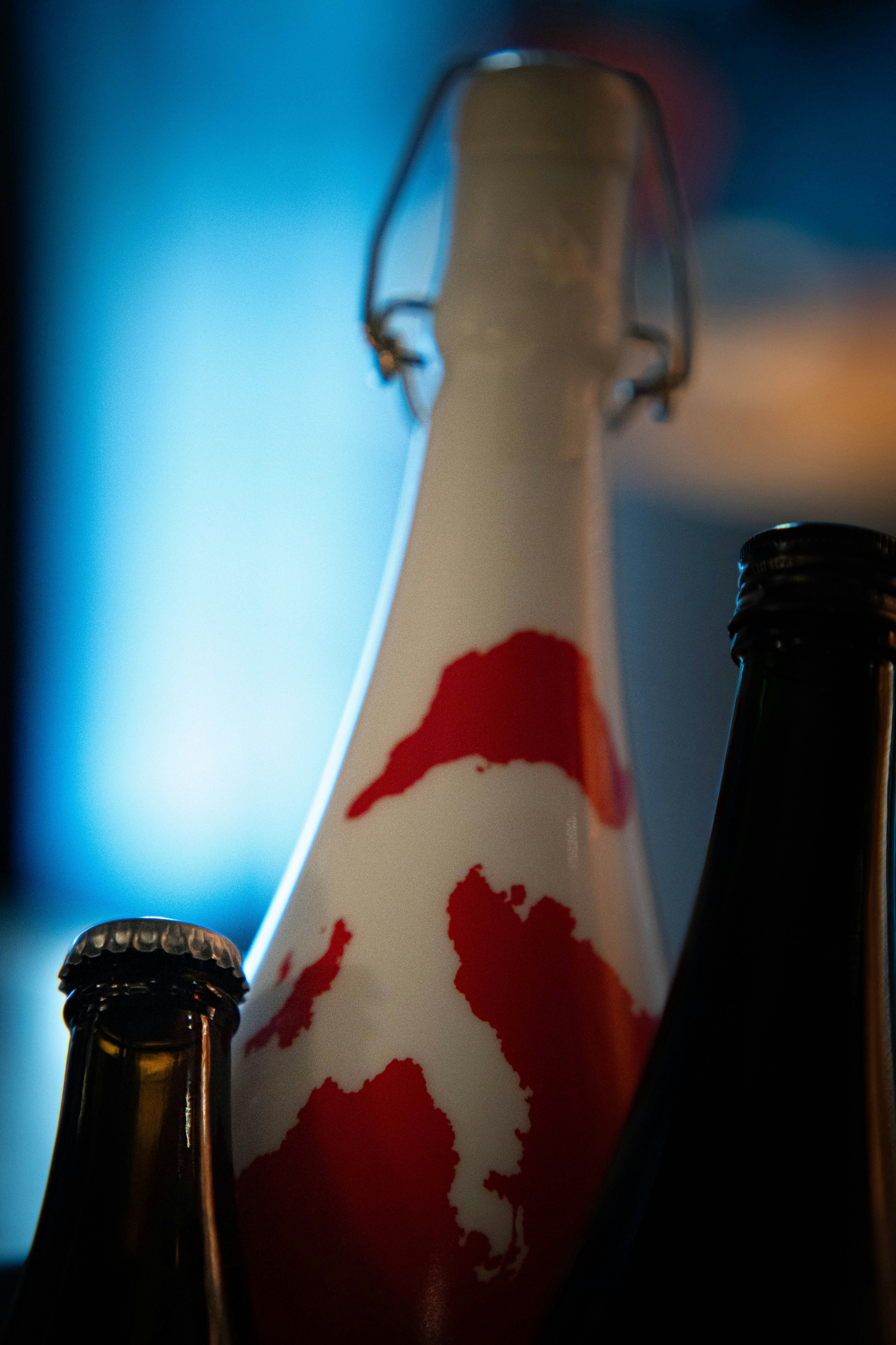 A strikingly designed bottle with red patterns stands prominently among darker bottles, illuminated by soft ambient light.