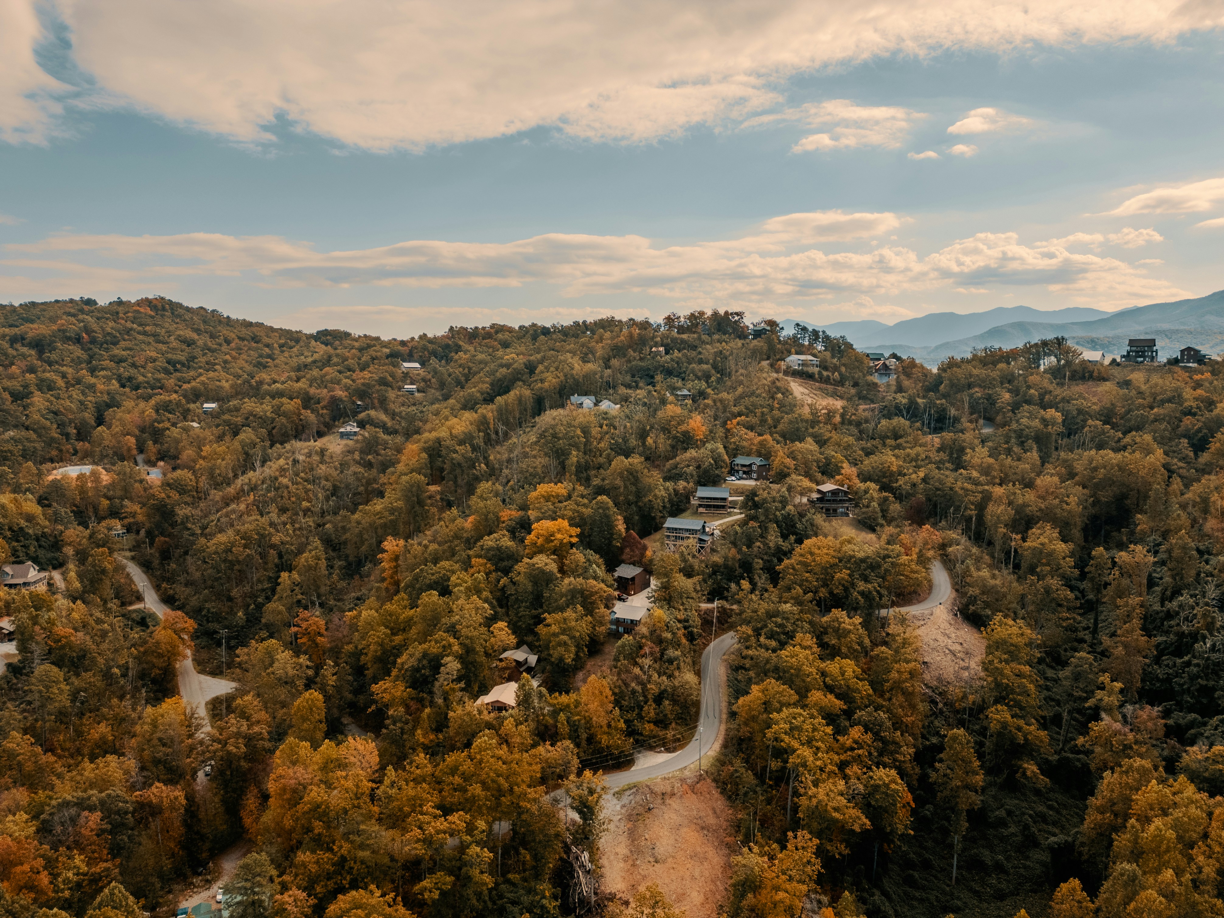 Aerial view of winding roads meandering through a vibrant autumn landscape, showcasing a blend of colorful foliage and residential structures.