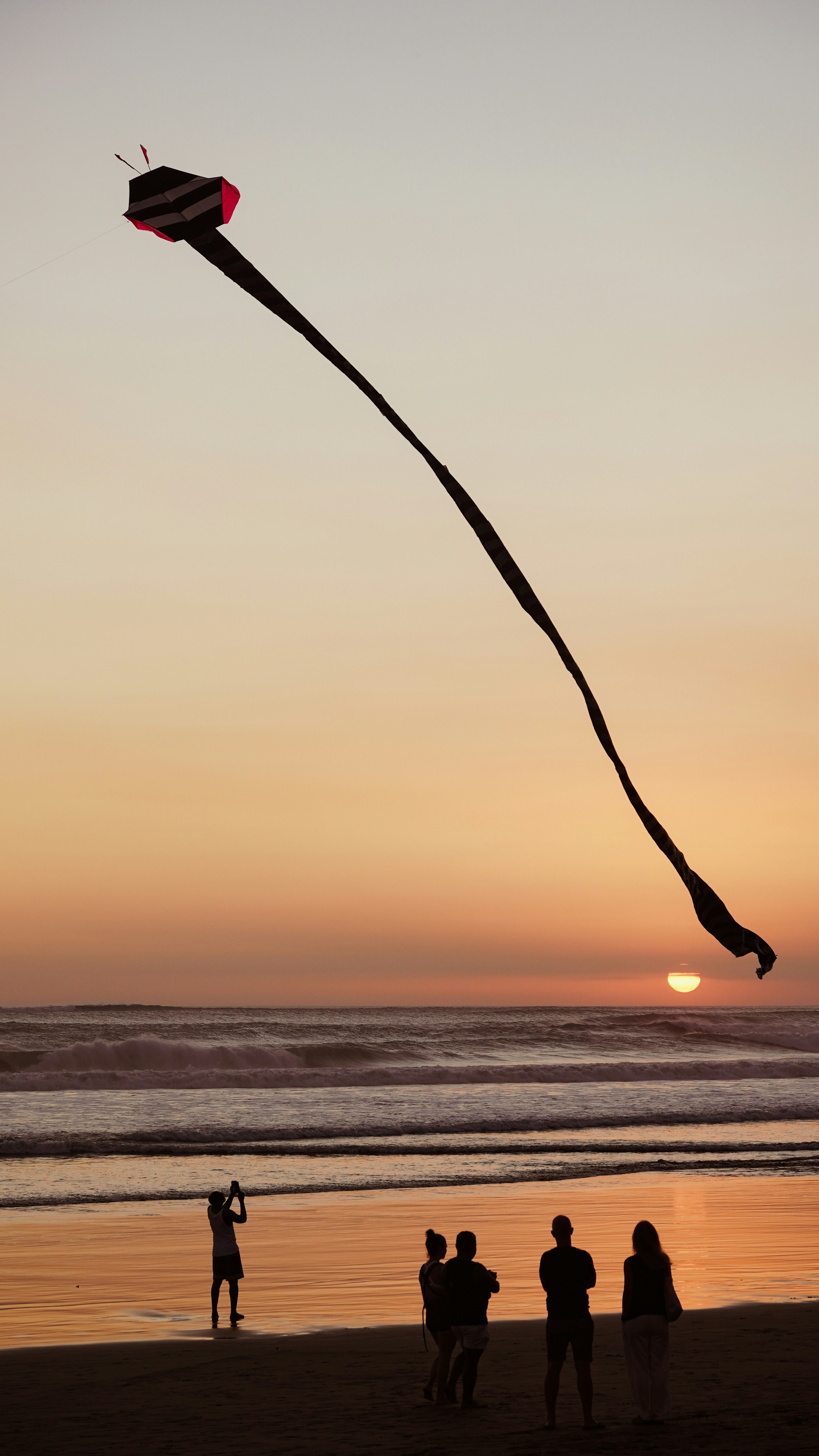Kite flying over beach at sunset with people watching