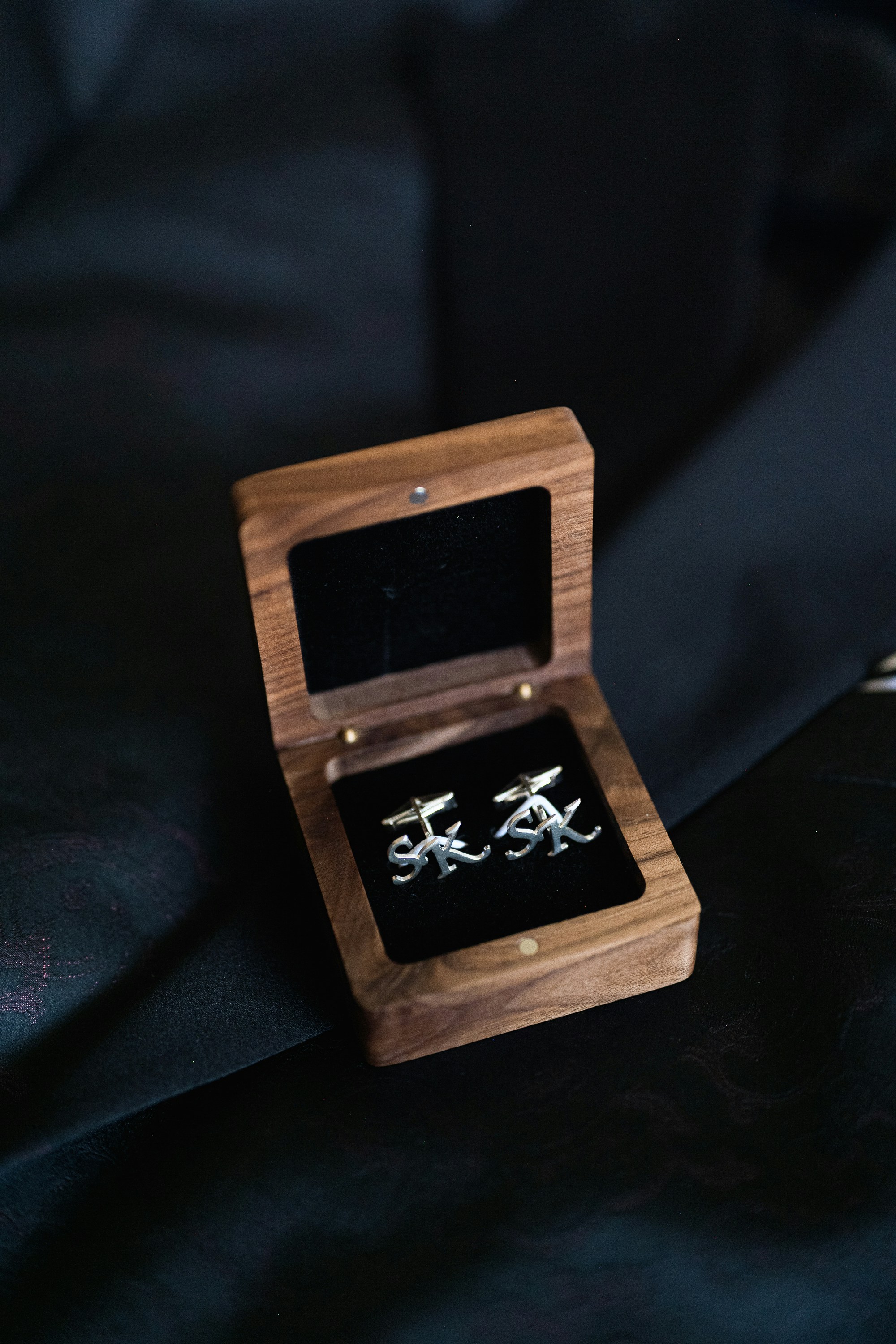 Wooden box containing silver cufflinks against a dark fabric backdrop.