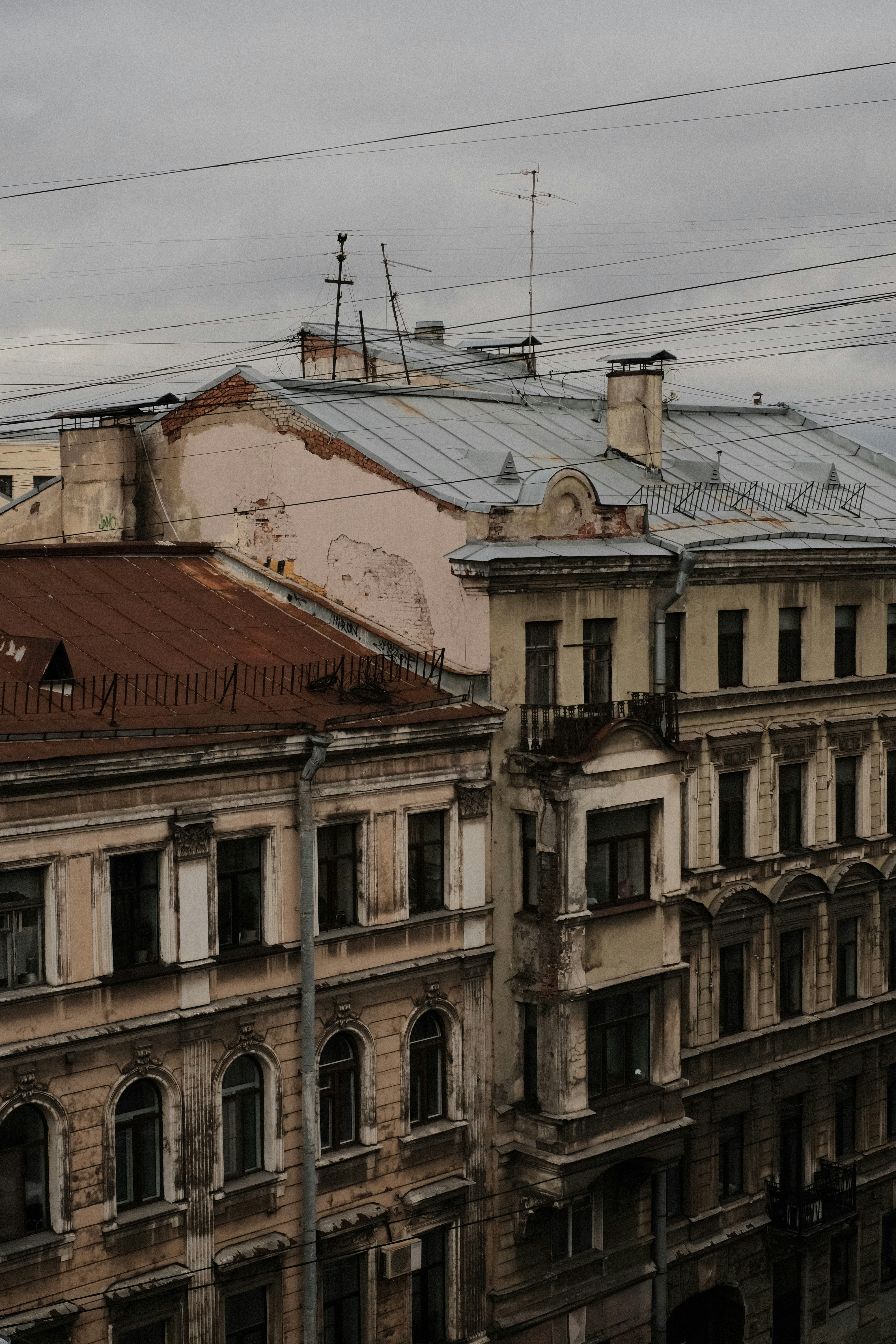 The facade of an old architecture of Saint Petersburg, a view of roofs and wires | Old apartment buildings under a cloudy sky