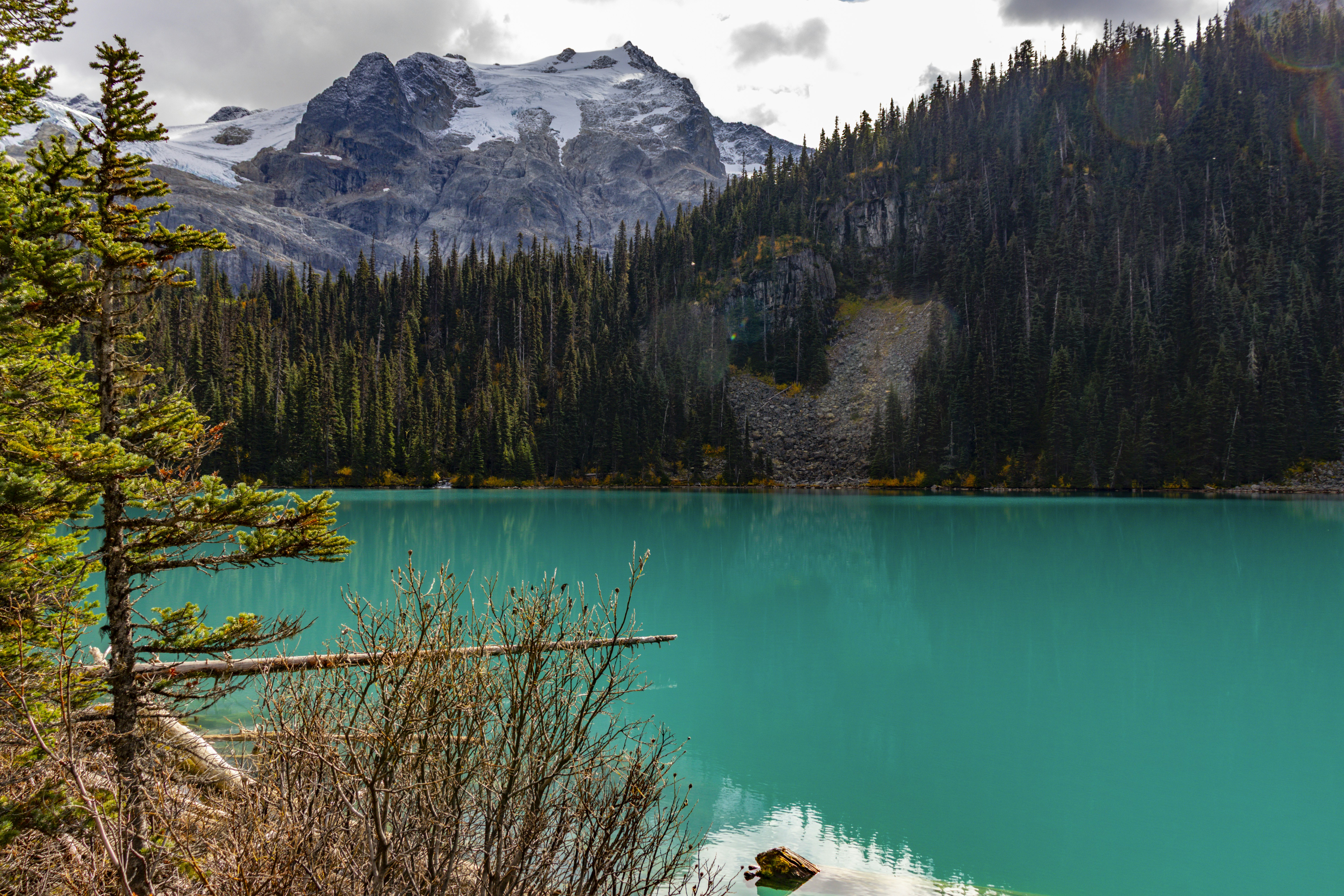A turquoise blue lake nestled in the forest beneath a glacier capped mountain. 2025-10-04 Joffre Lakes, British Columbia, Canada | Turquoise lake with snow-capped mountains and pine trees