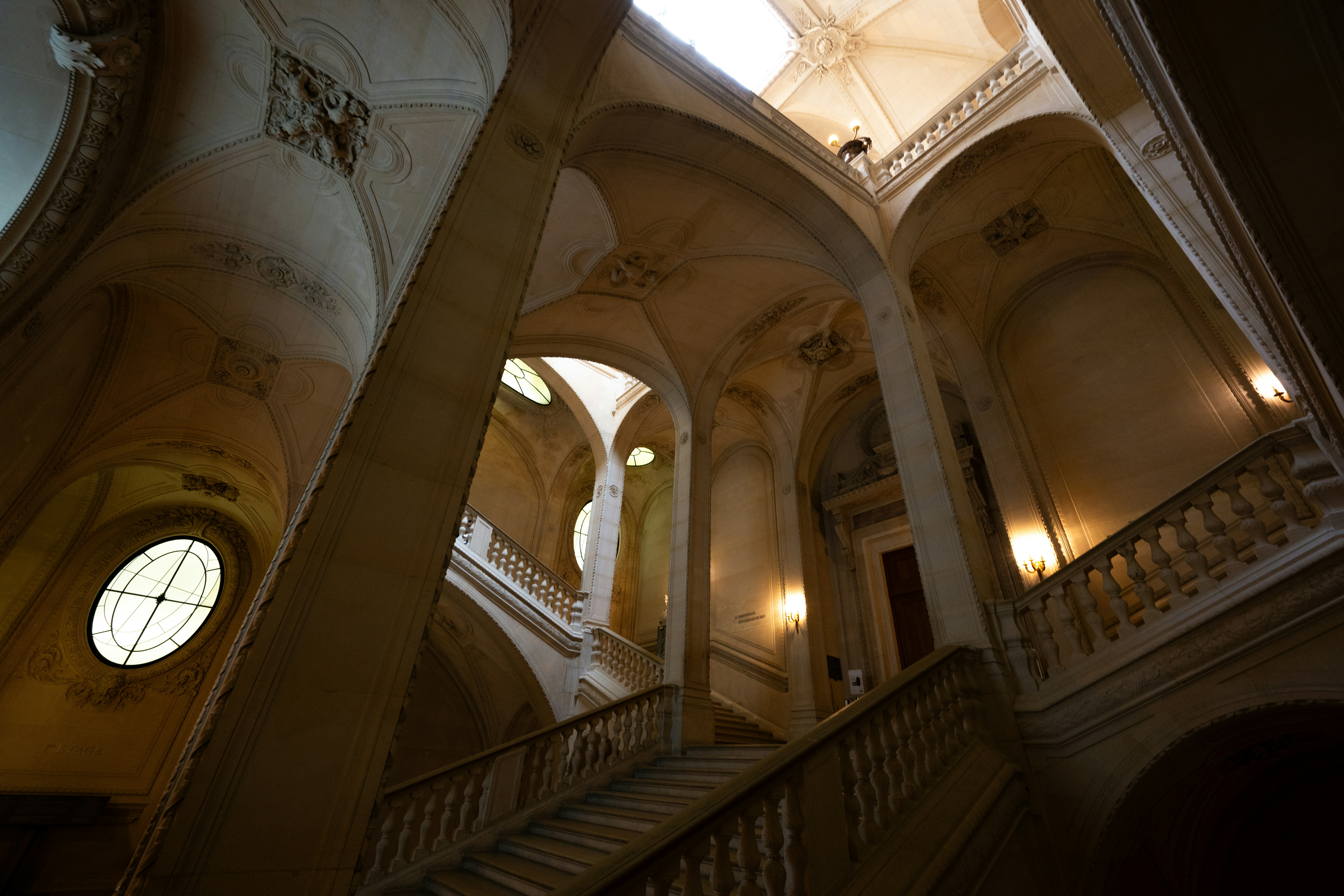 Intricate architectural details of a grand staircase illuminated by soft light, showcasing elegant arches and a circular window.