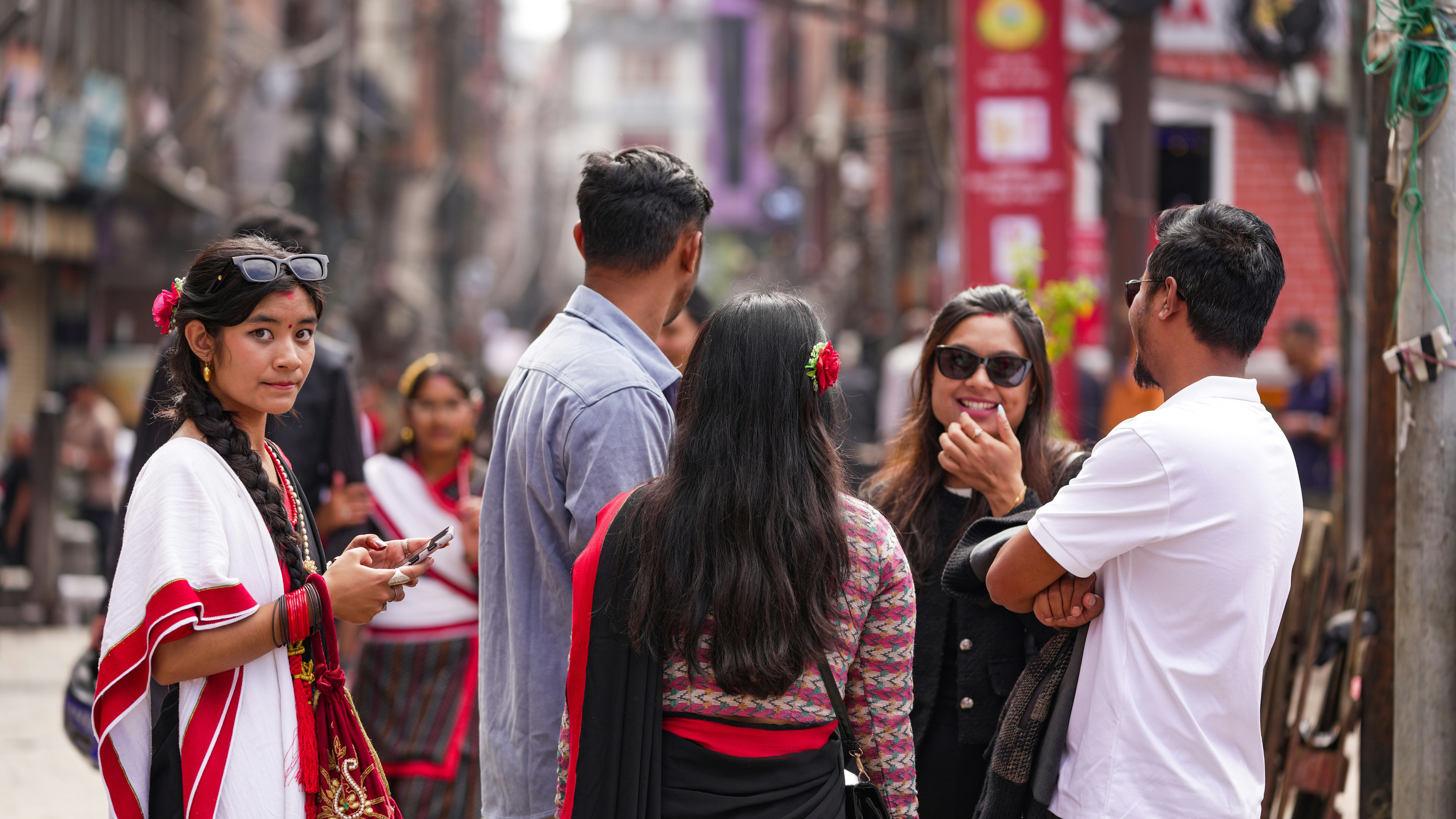 Group of people engaging in lively conversation on a bustling street in Kathmandu, showcasing traditional attire and vibrant local culture.