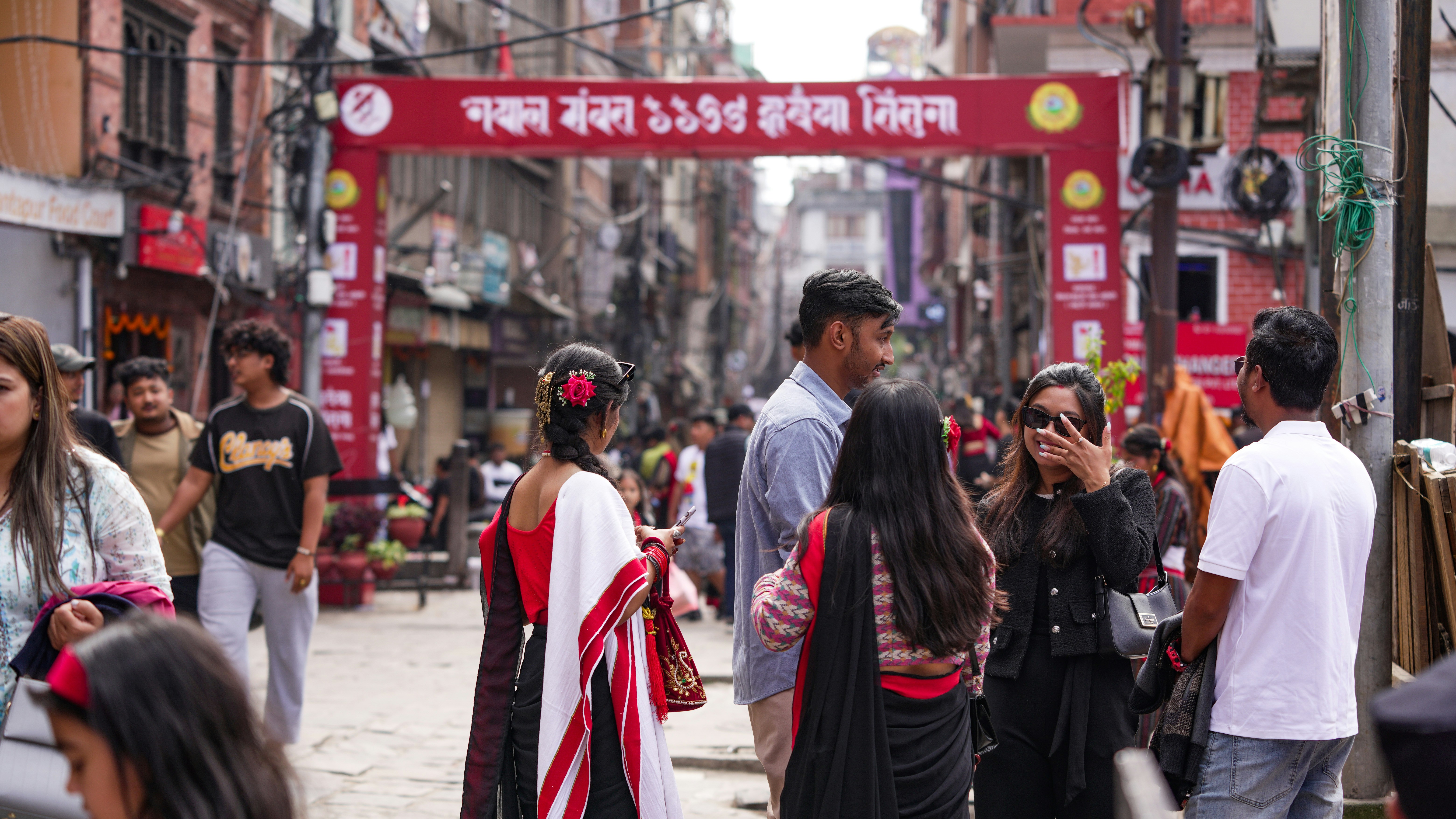Crowd of people engaging in lively conversation under a vibrant archway in Kathmandu, showcasing local fashion and community spirit.