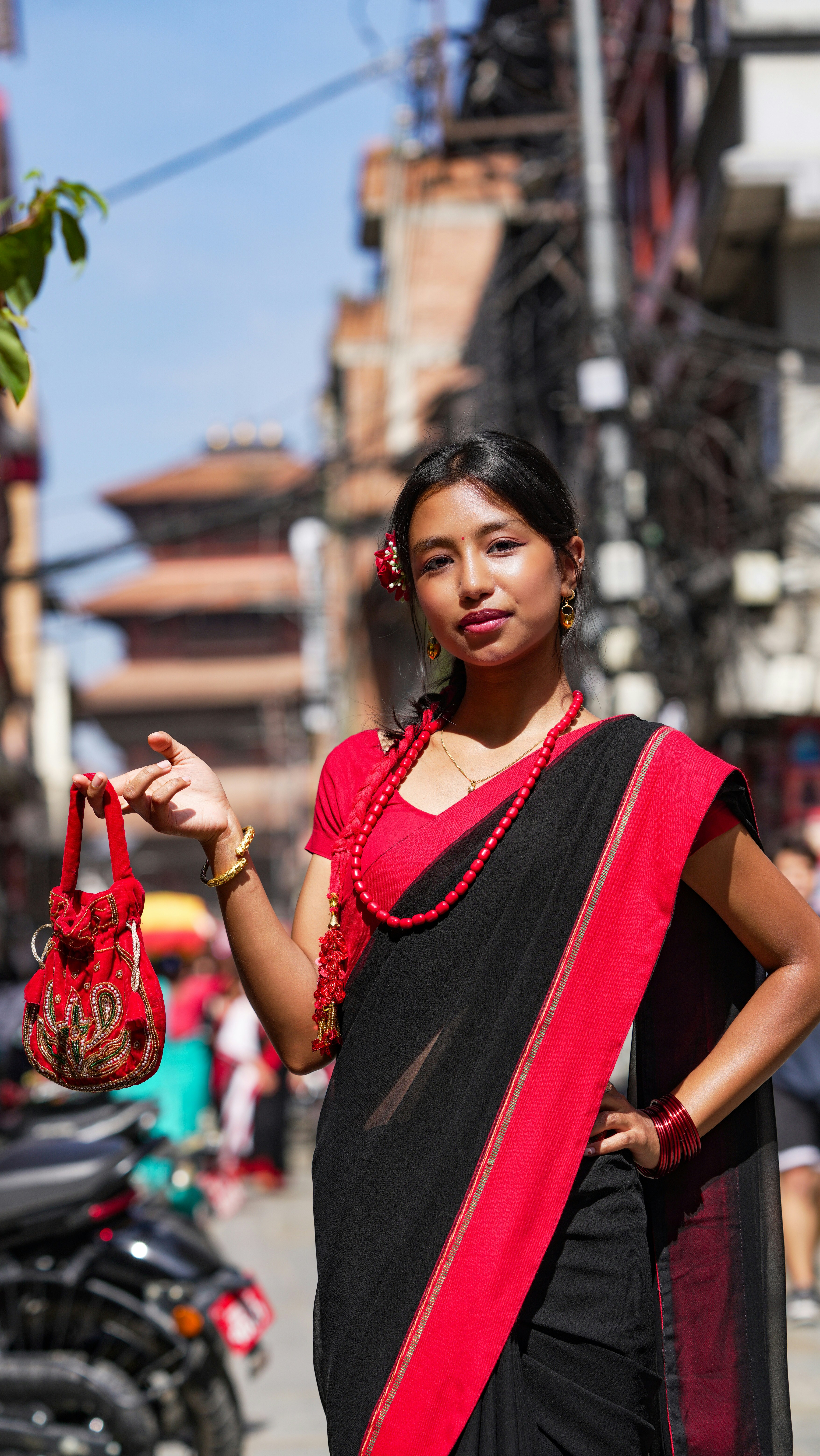 Woman in traditional attire holding a decorative handbag against a bustling city backdrop. The scene reflects a blend of culture and modernity.