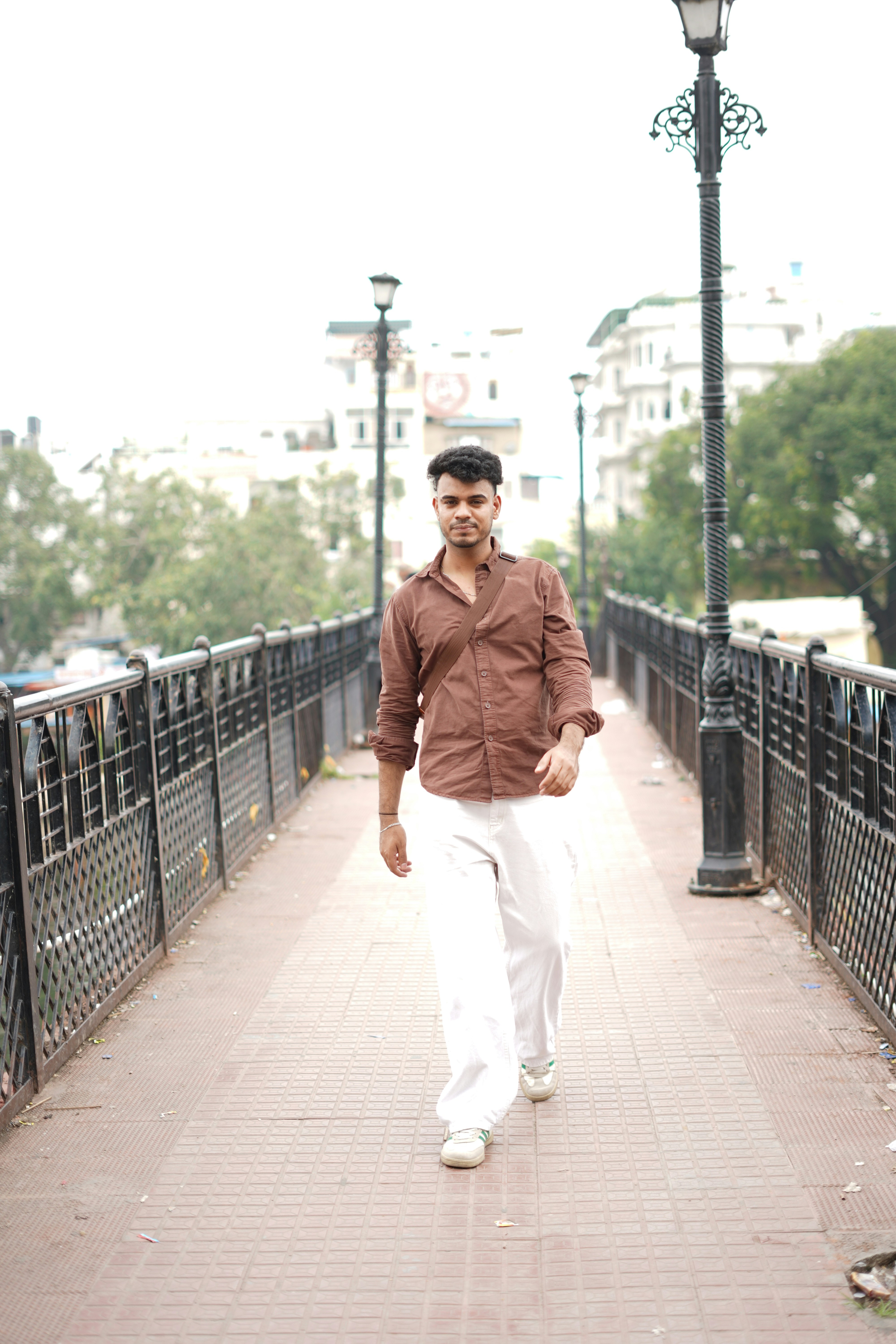 A man walks on a bridge with lampposts.