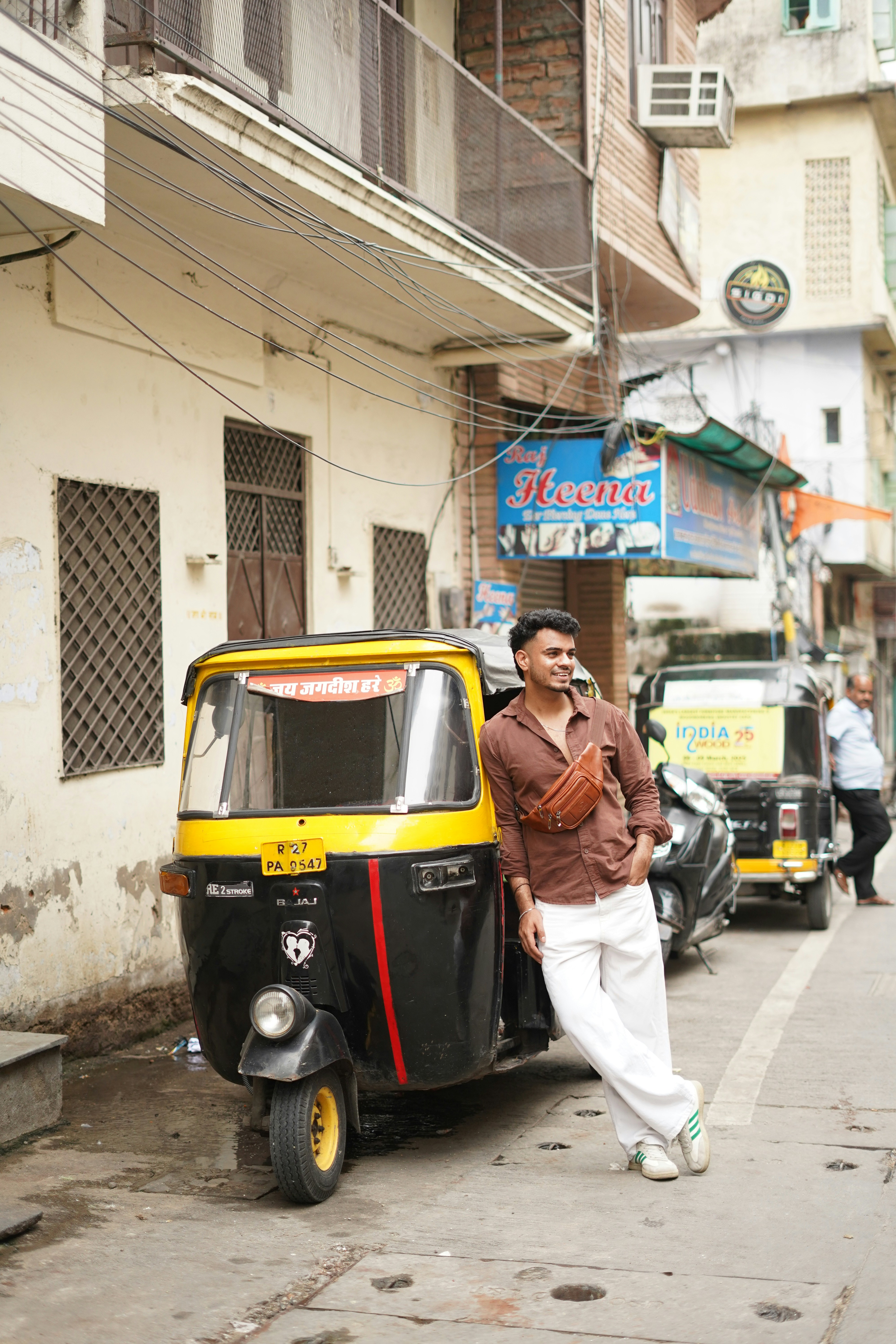 Man leaning on auto rickshaw on a street.