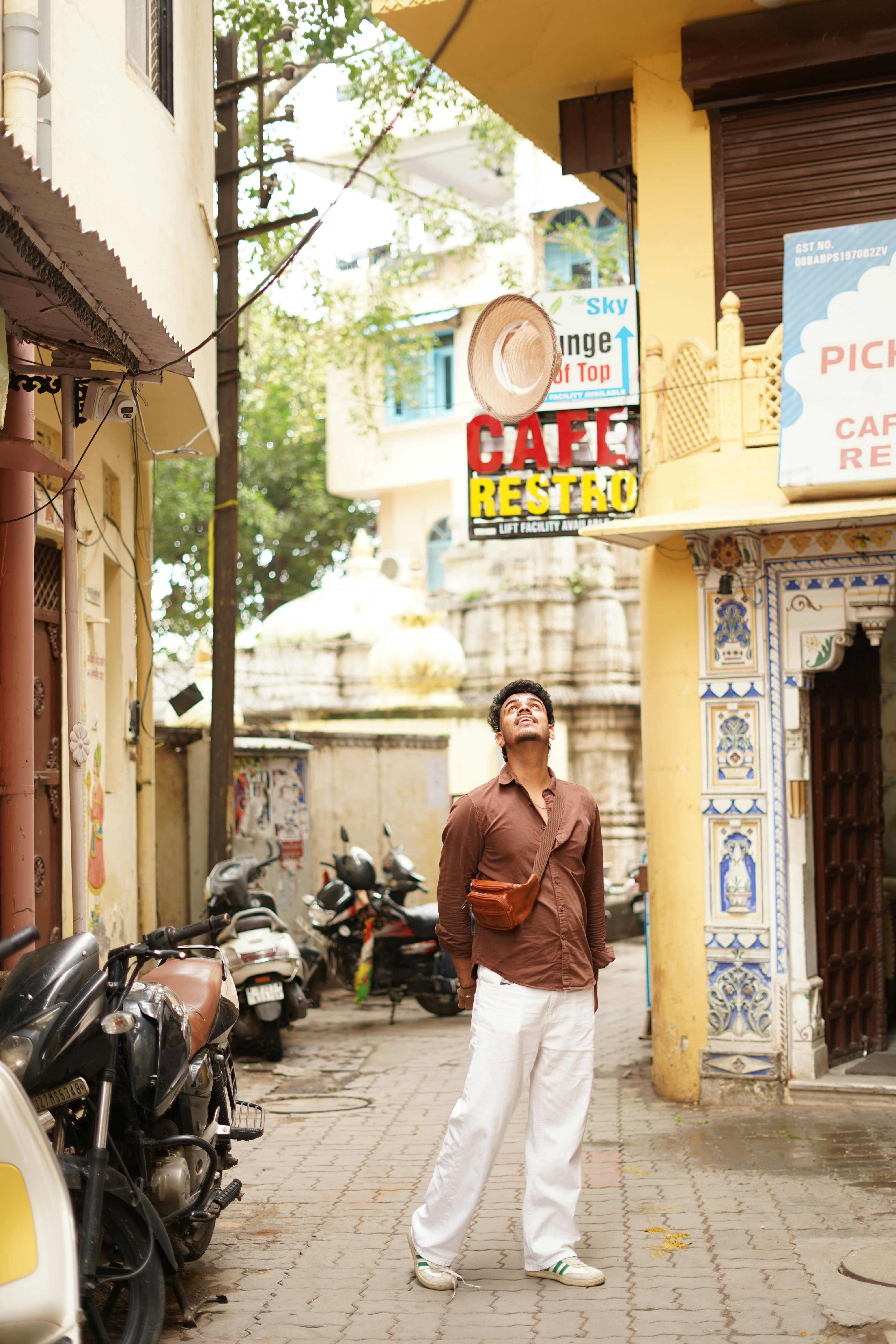 A man gazes upward in a bustling street, surrounded by parked motorcycles and vibrant storefronts. The scene captures the essence of urban life and introspection.
