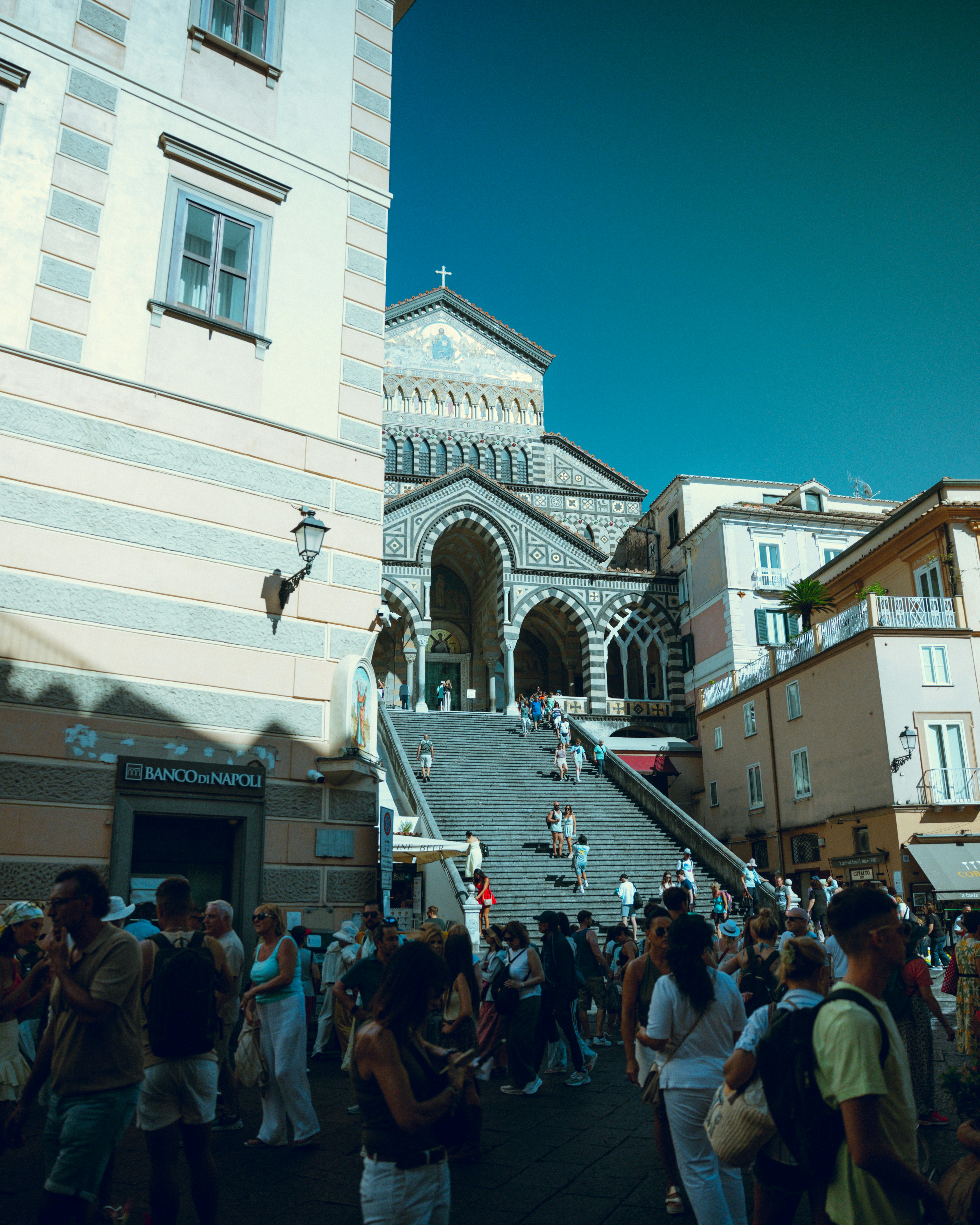 Historic cathedral steps bustling with people, framed by charming architecture under a clear blue sky.