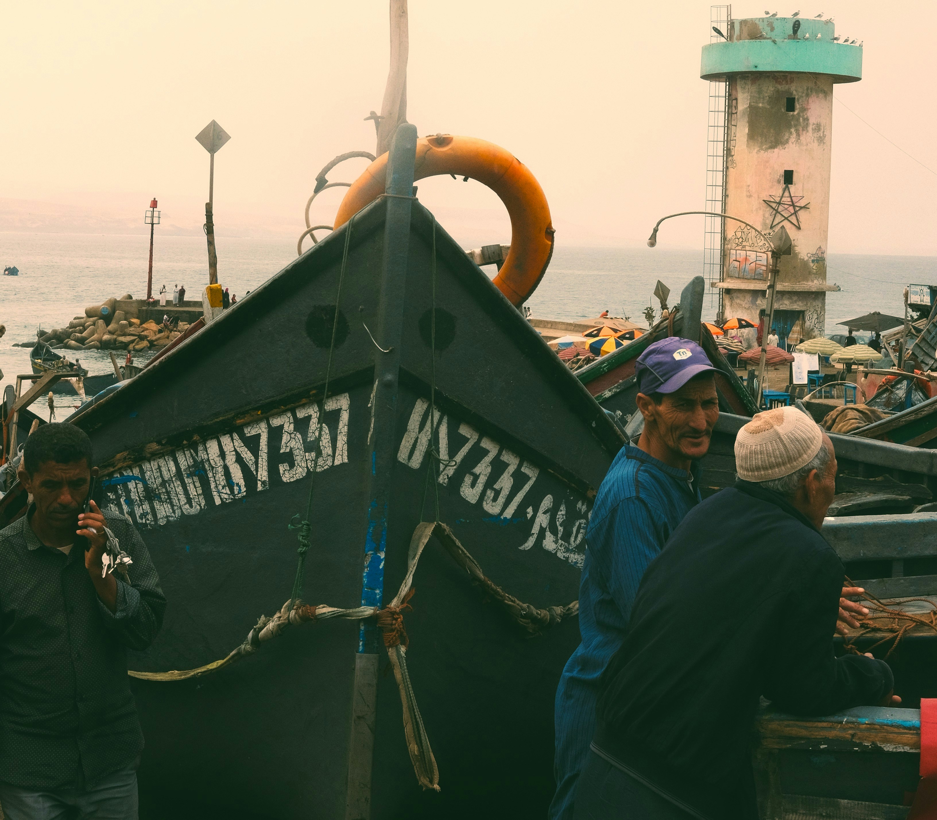 Harbor at Dusk: A Blue Hull, Fishermen, and a Distant Lighthouse