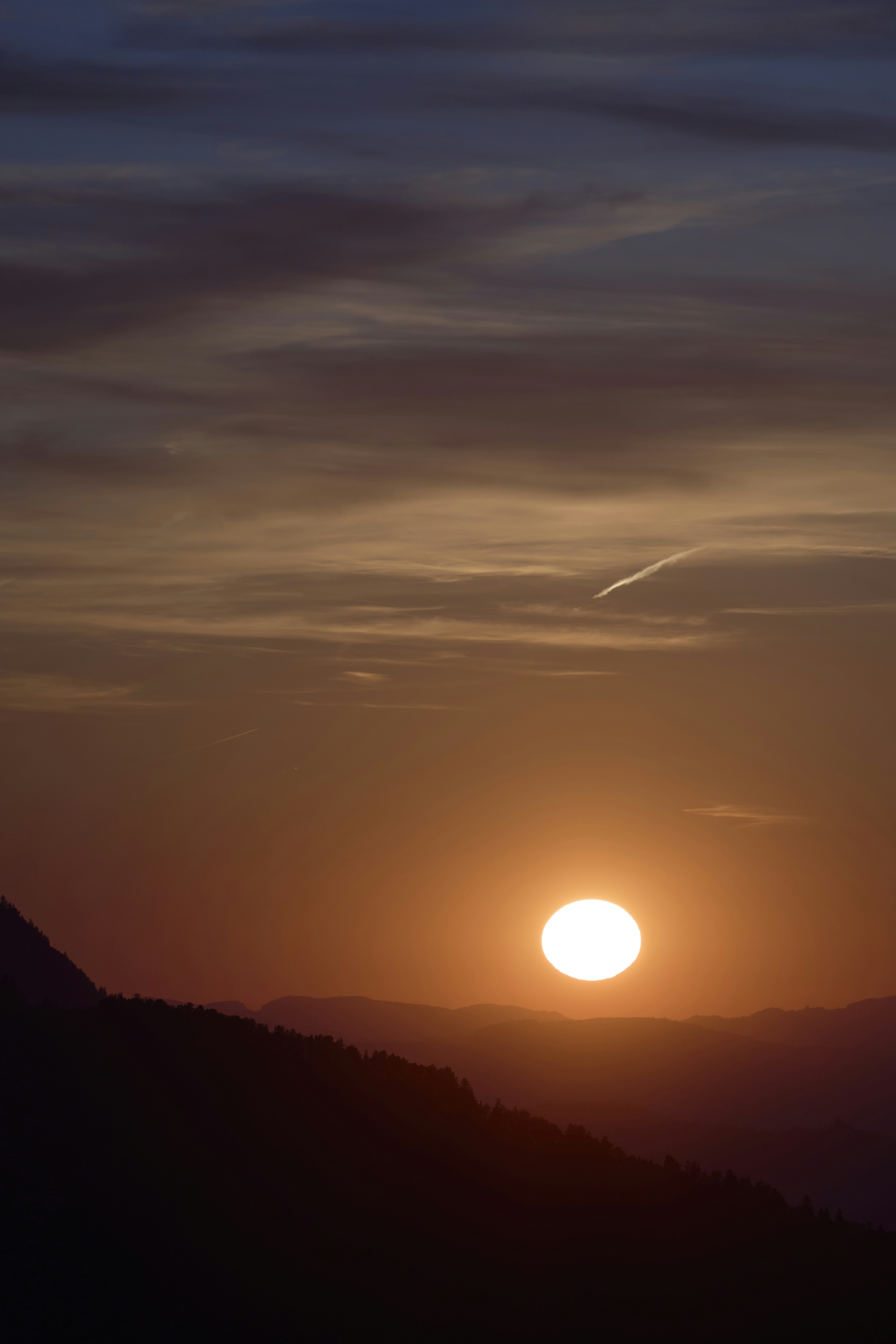 The sun sets behind a silhouetted mountain range.