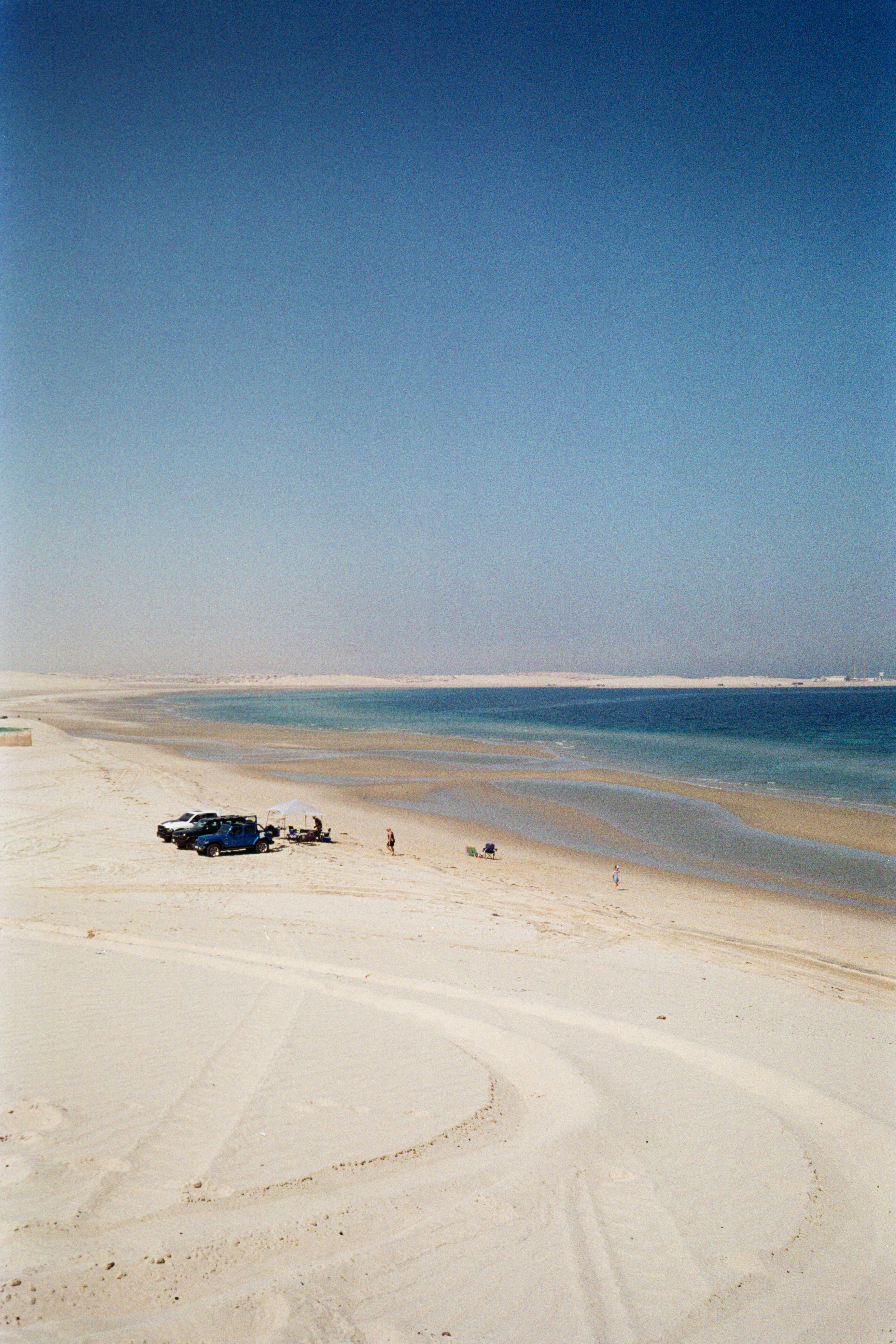 Kodak Gold 200 🎞️ | Deserted beach with vehicles and people near the ocean.