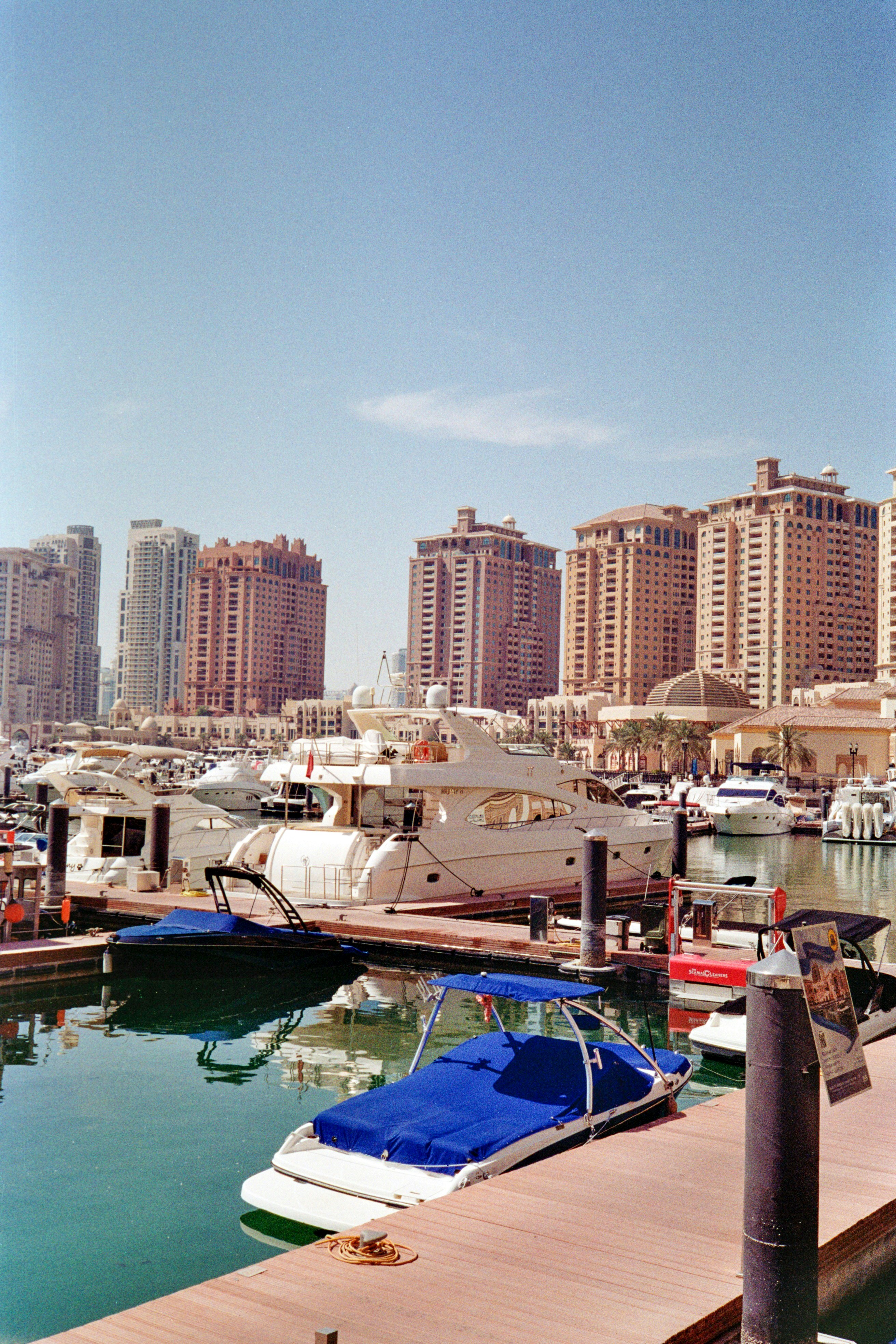 Luxury yachts docked at a vibrant marina surrounded by modern high-rise buildings under a clear sky.