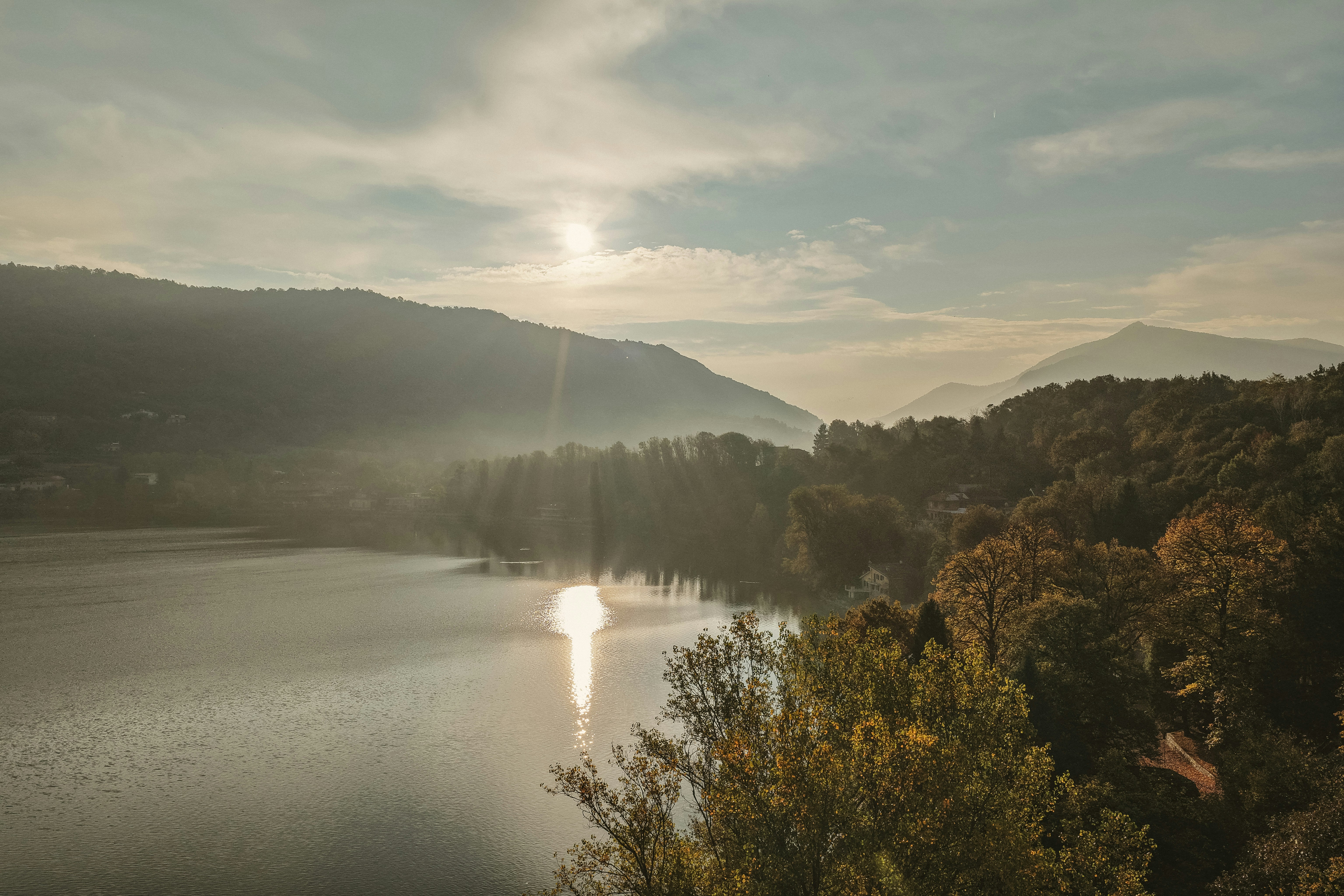 Gentle morning light reflecting on a serene lake surrounded by misty mountains and lush trees. The soft glow creates a peaceful atmosphere.