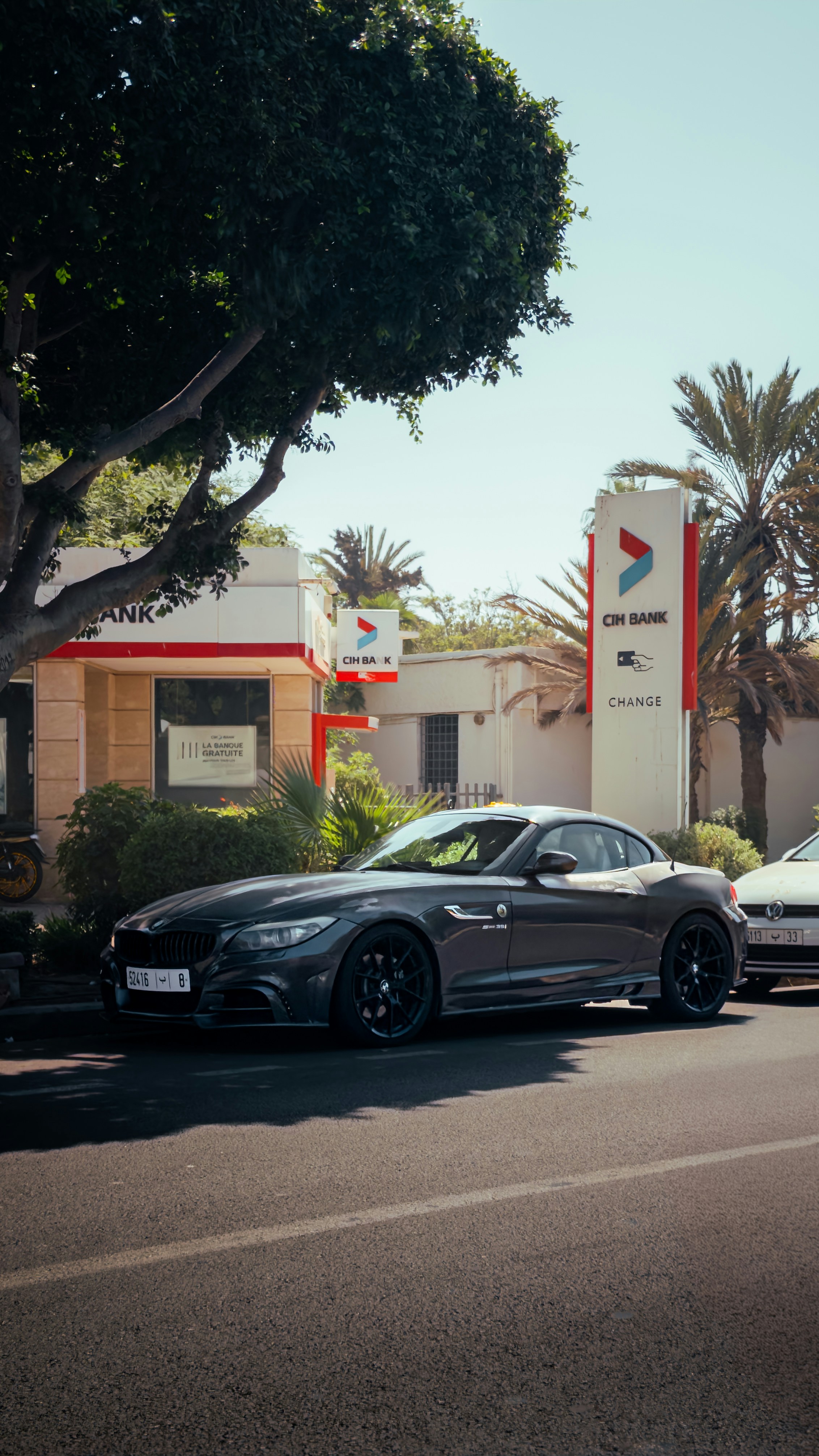 Dark grey sports car parked near a bank.