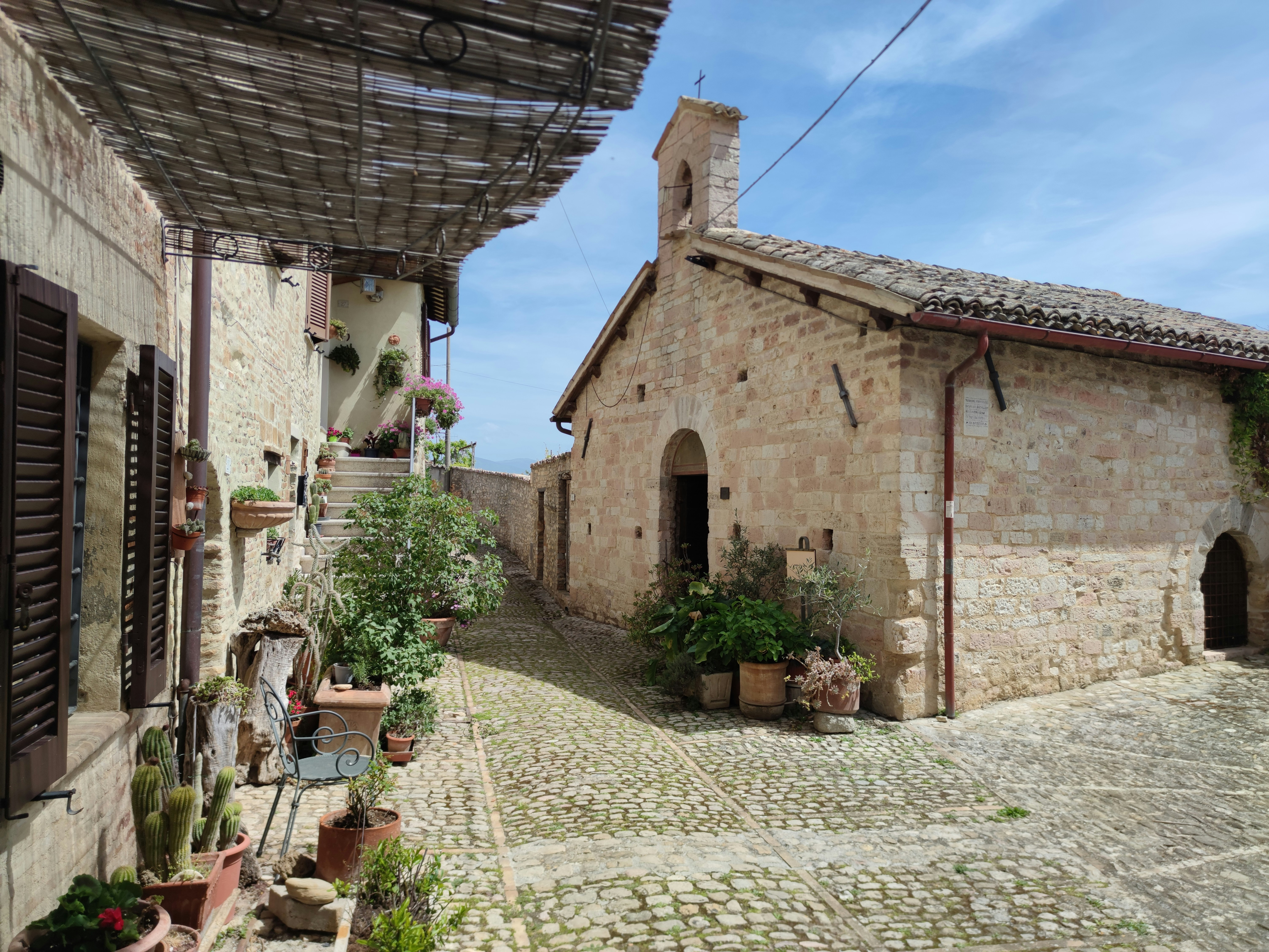 Quaint stone buildings and lush greenery create a serene courtyard atmosphere in a rustic village setting.