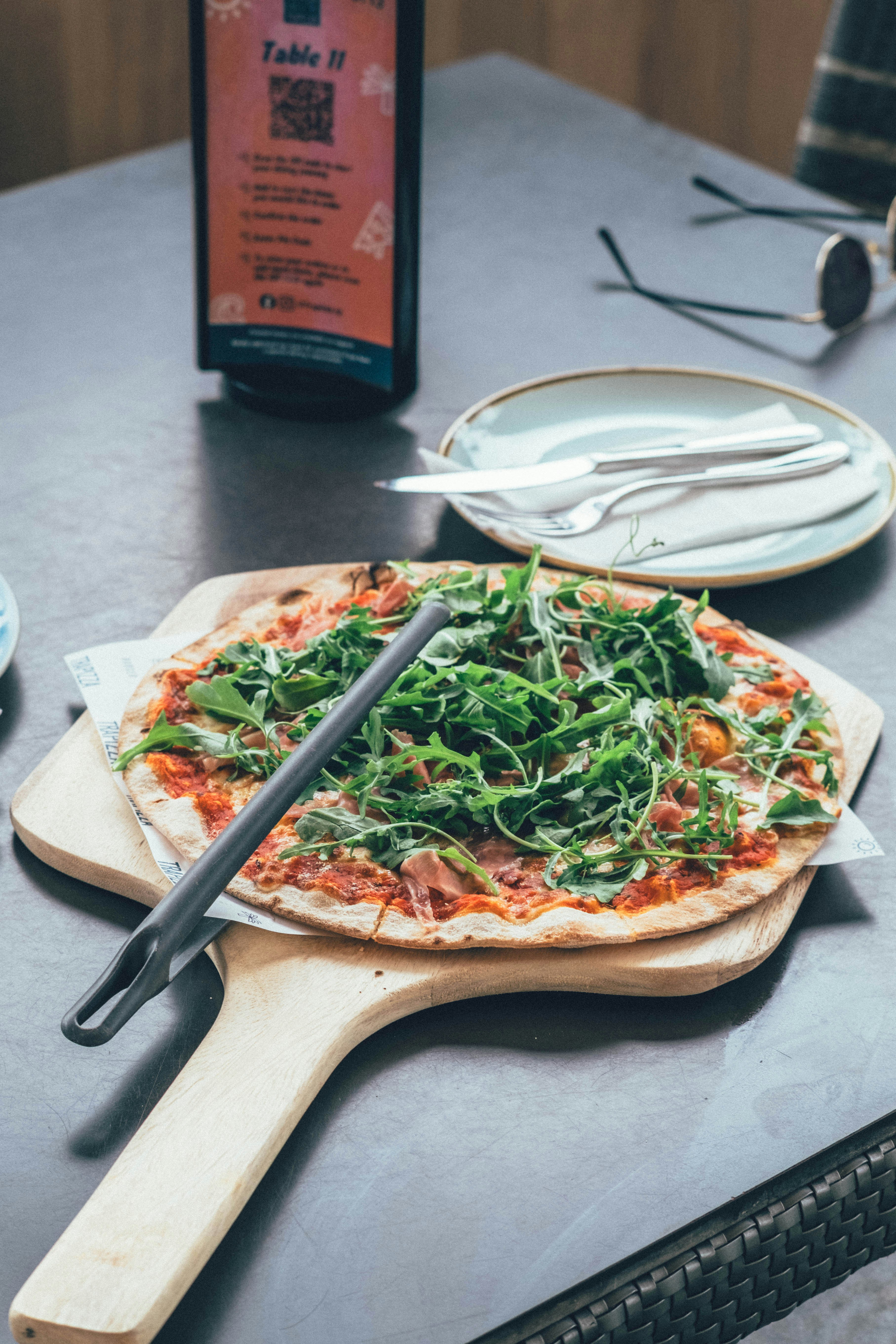 Arugula pizza on a wooden peel with tongs.