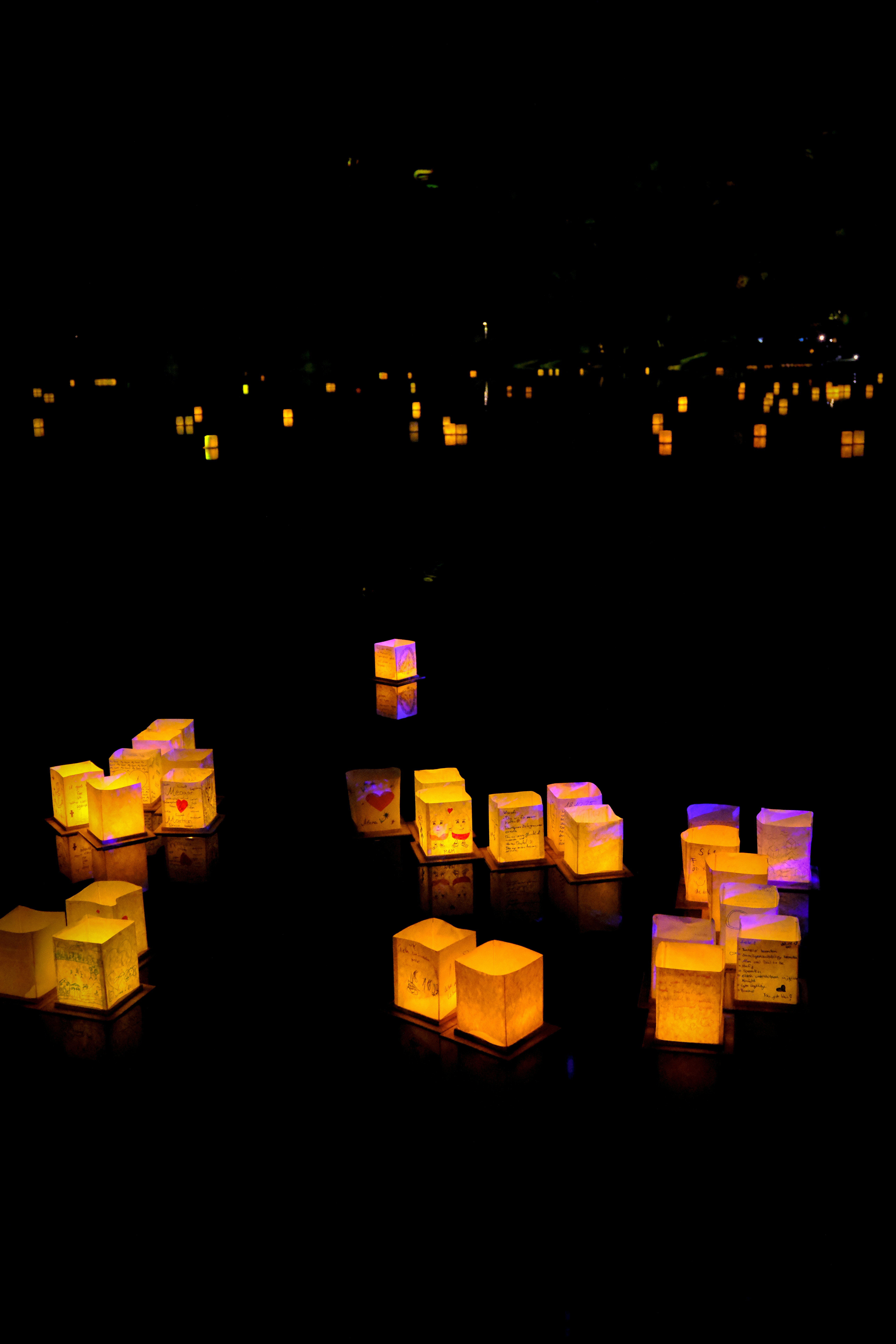 Floating lanterns glow on dark water at night.