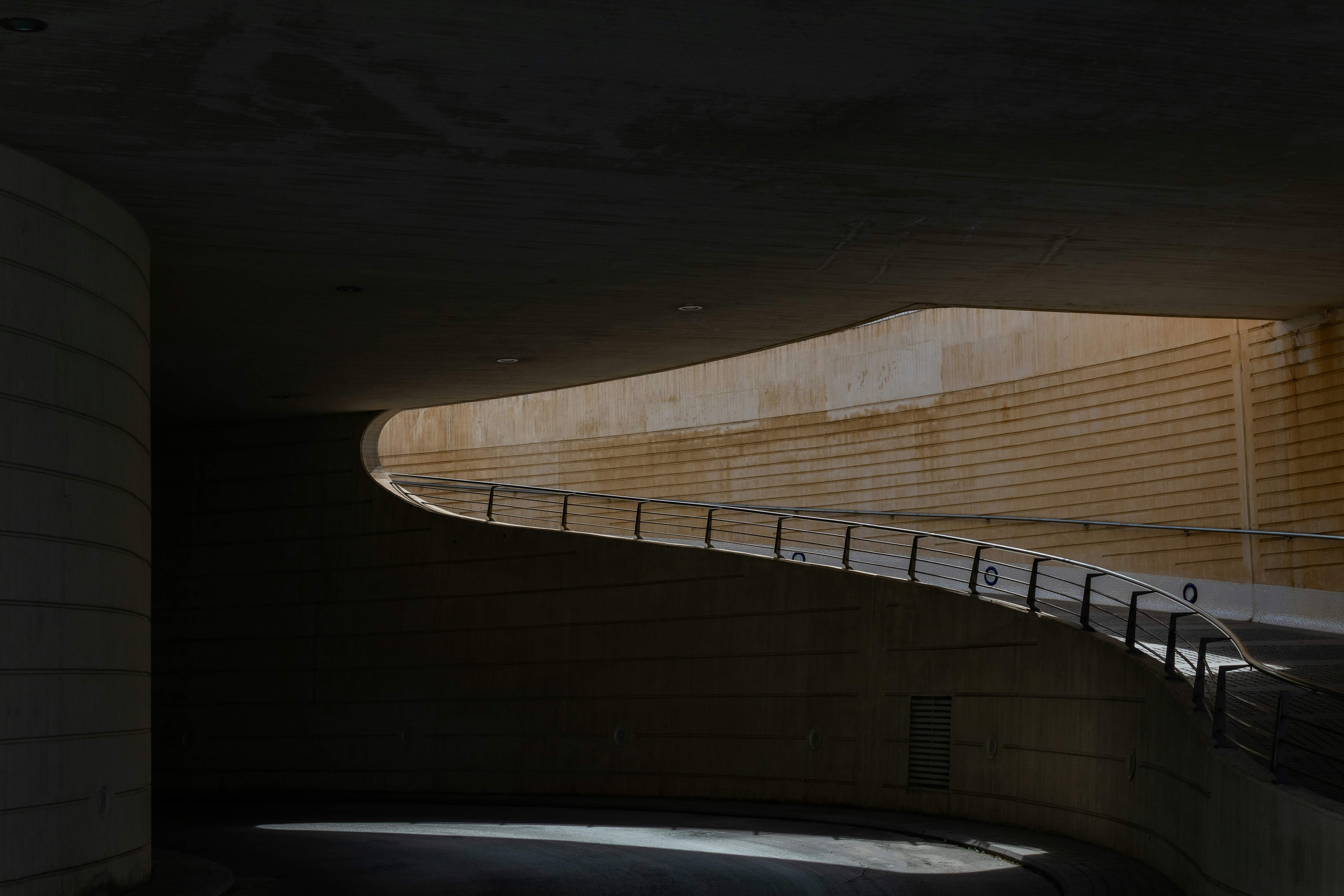 Architectural interior featuring a smooth, curved ramp illuminated by soft light, creating a dynamic interplay of shadows and textures.