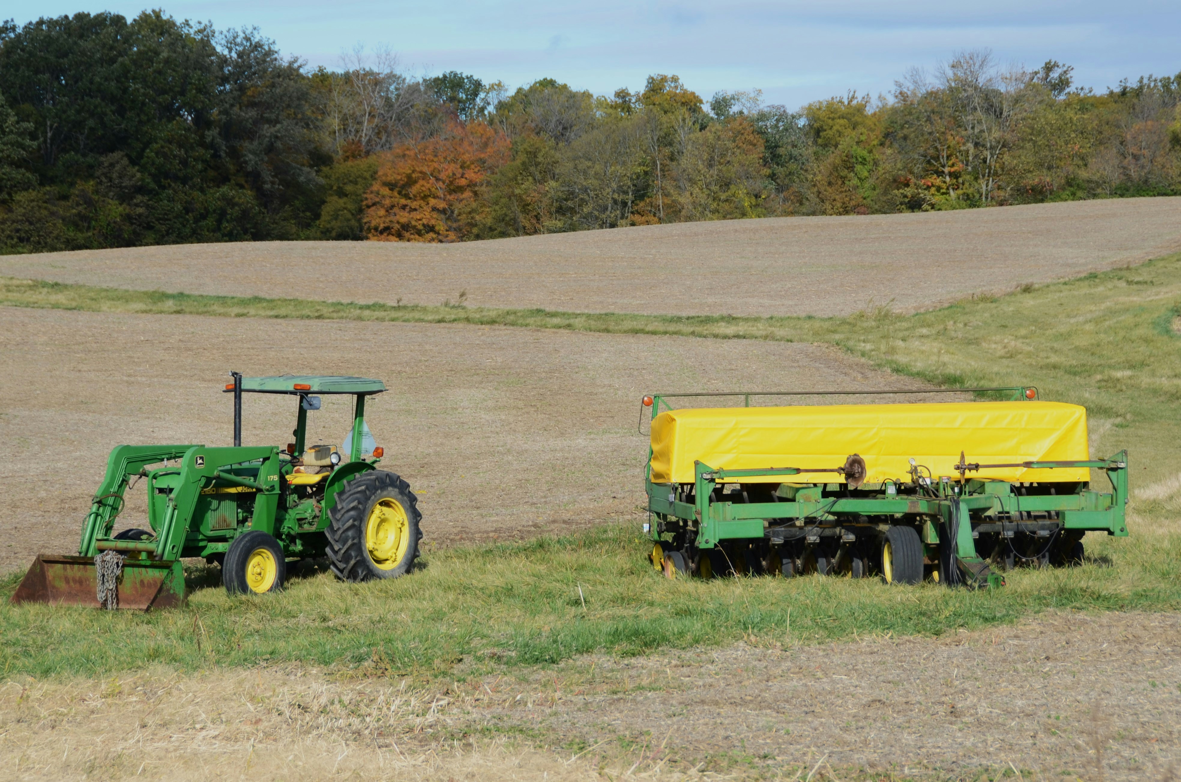Idle Green Tractor with Yellow Drill in a Quiet Harvest Field