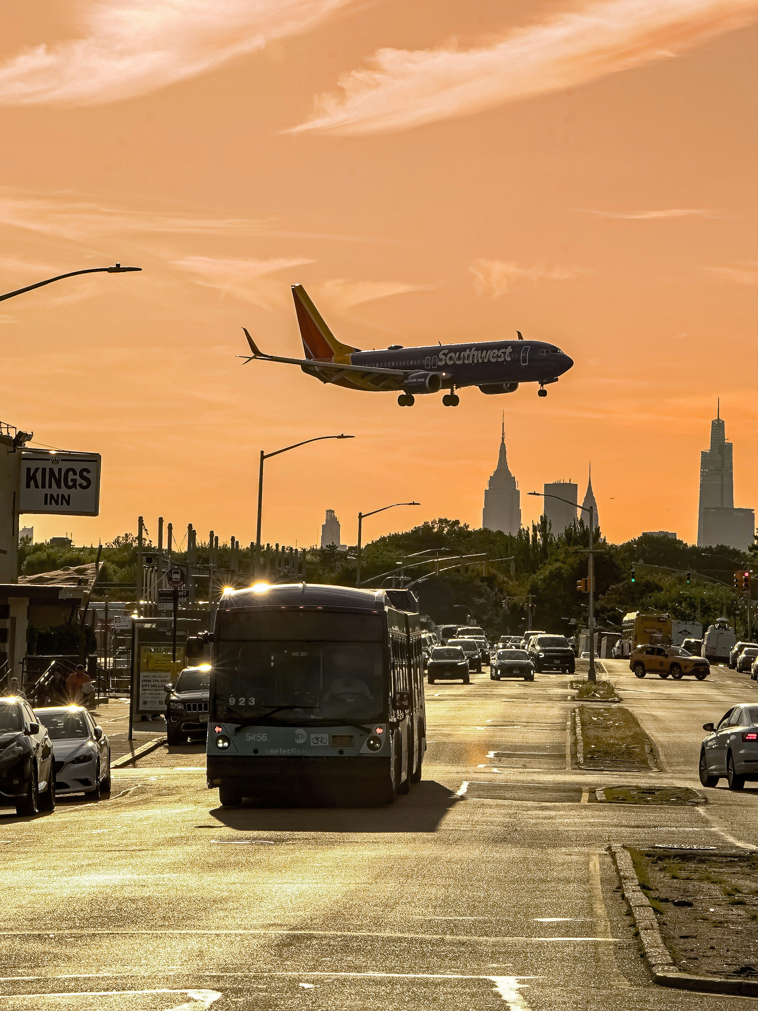 Road to Orange Skies - SMNYCMan | Airplane flying over busy street with city skyline