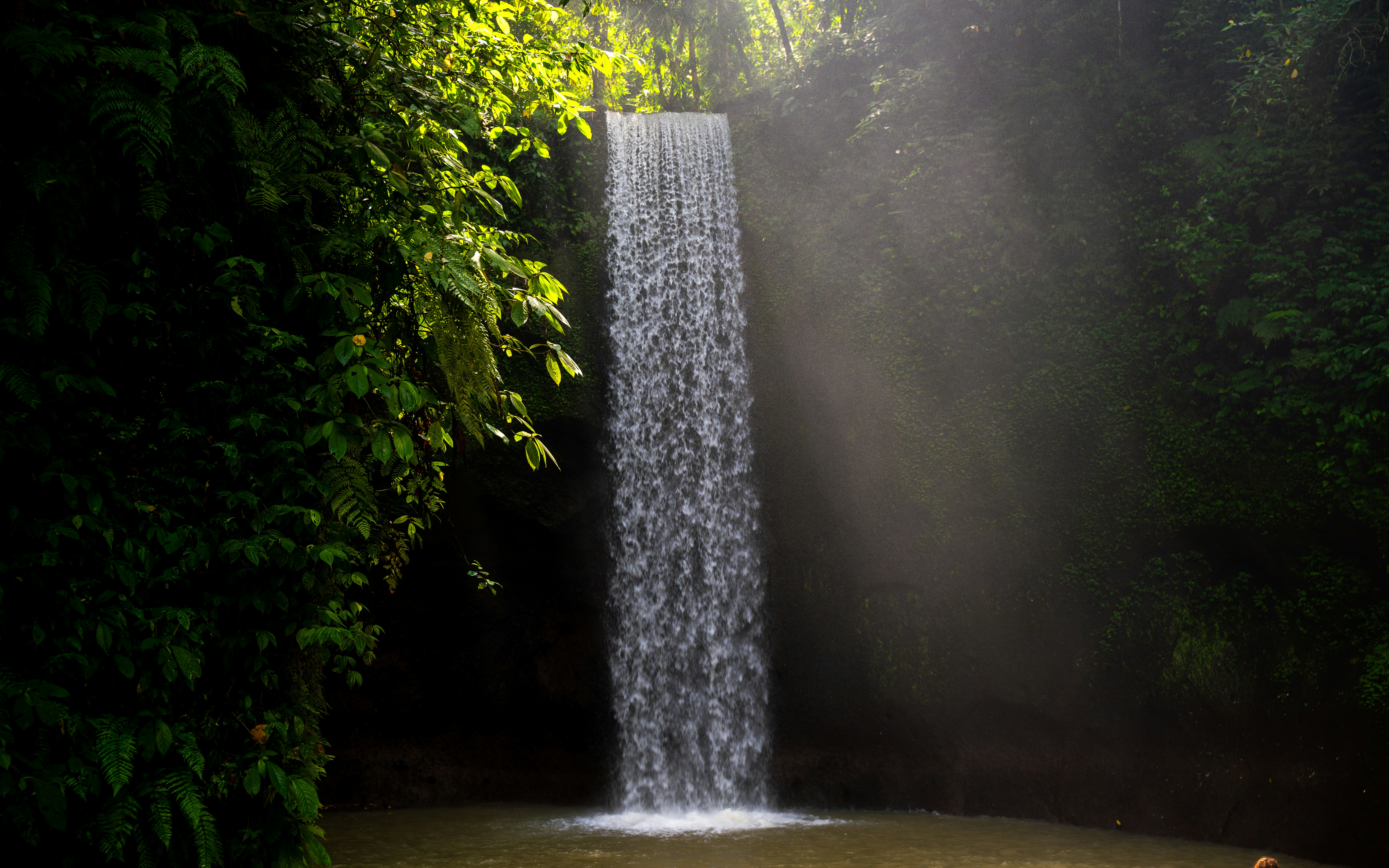 Majestic waterfall cascading down a rocky cliff surrounded by lush greenery and soft mist. The serene atmosphere invites tranquility.
