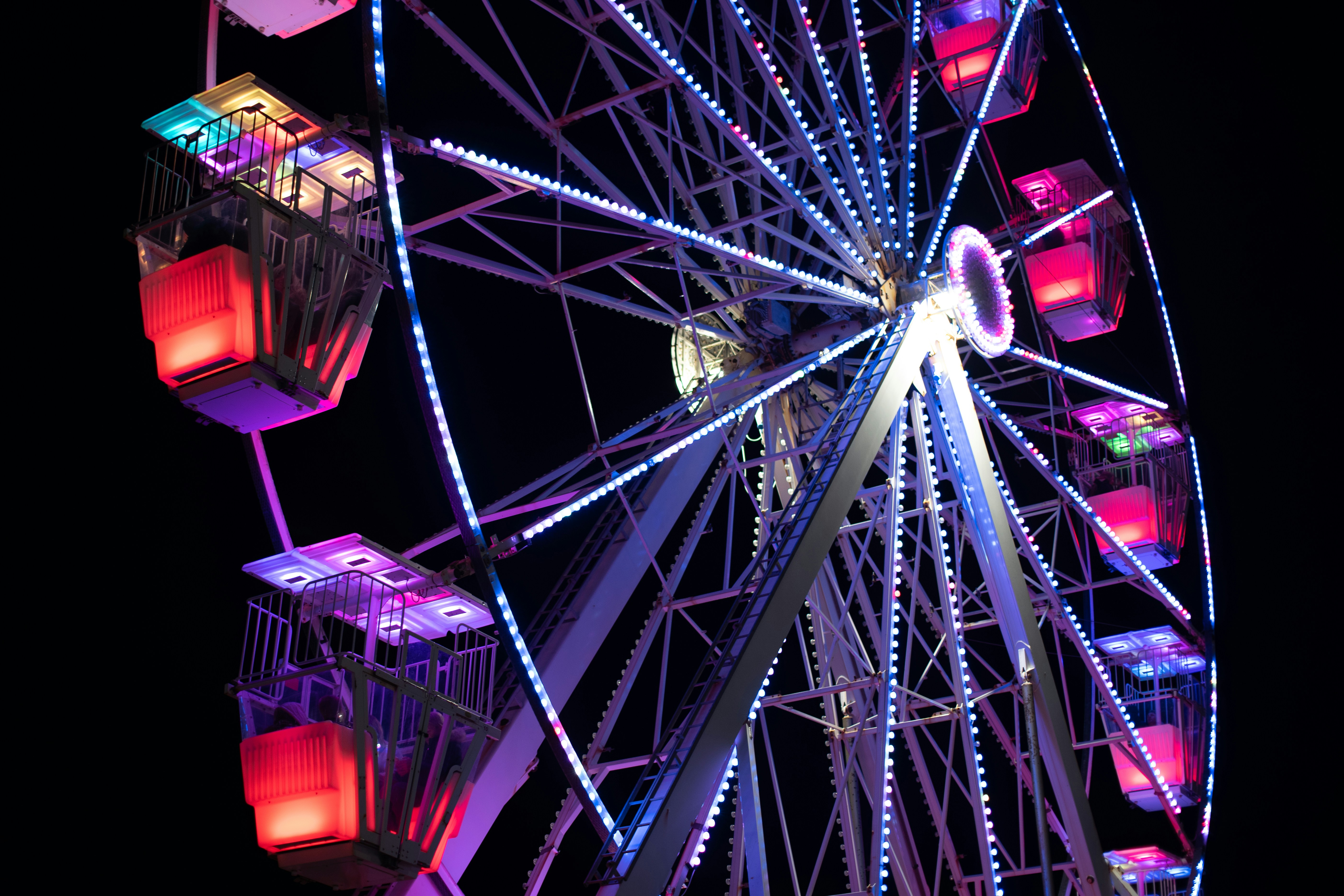 A brightly lit Ferris wheel glows against the night sky, with vivid neon colors reflecting off its metallic frame. | A brightly lit ferris wheel at night