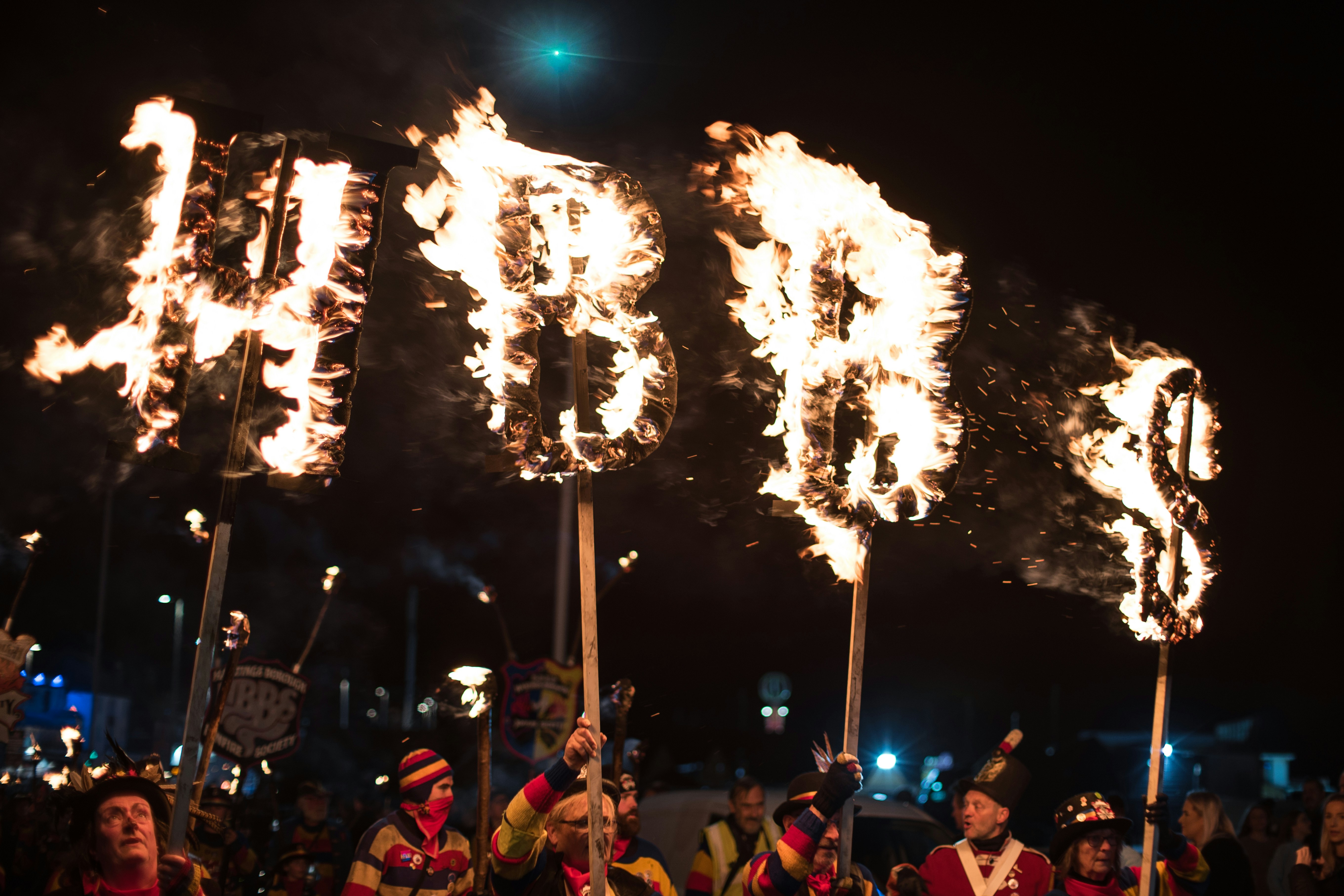 Participants holding flaming torches form the letters 'HBBS' during a vibrant night festival, showcasing community spirit and tradition.